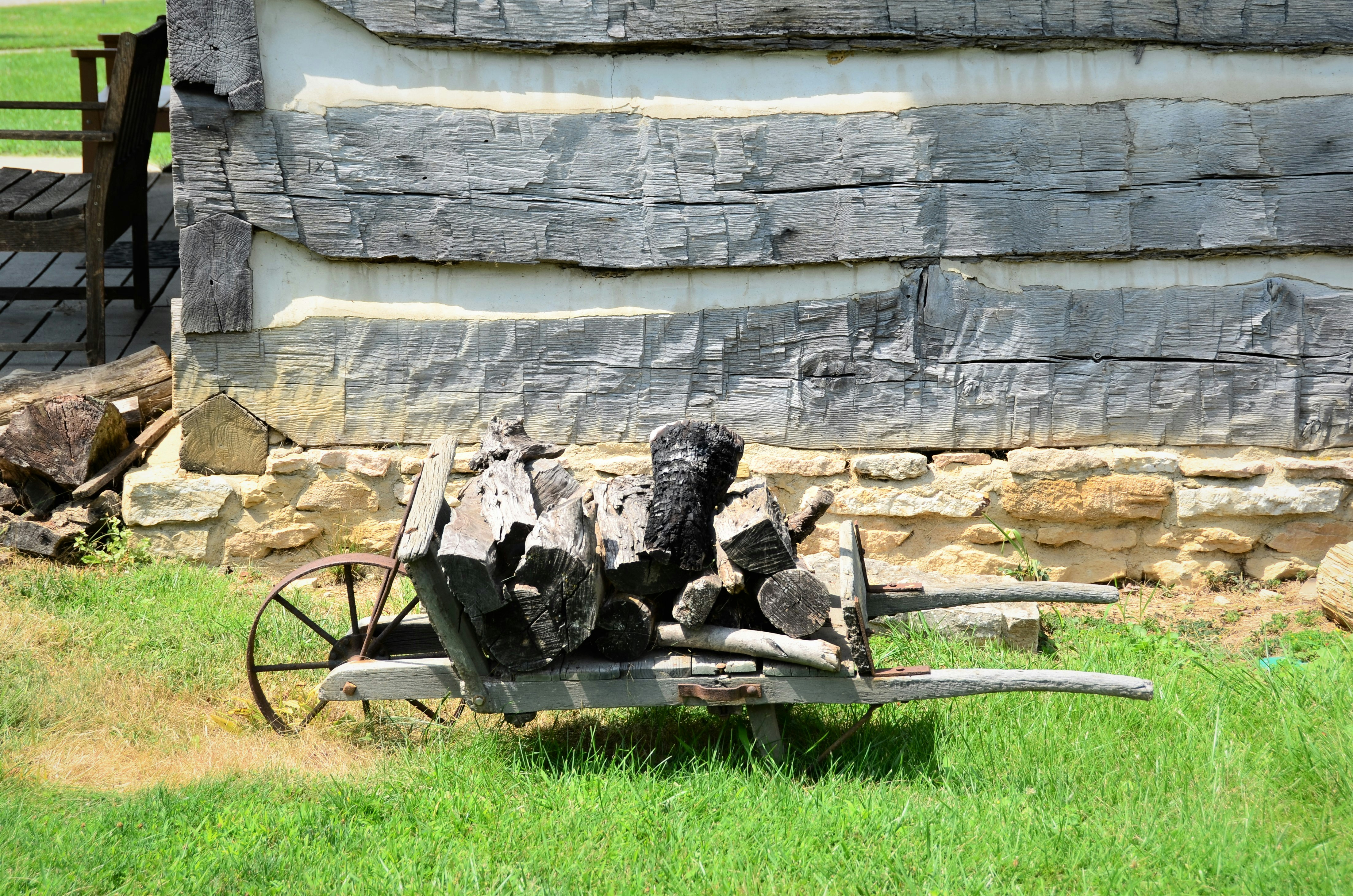 Charred Timber on a Weathered Wheelbarrow by a Rustic Log-and-Stone Homestead
