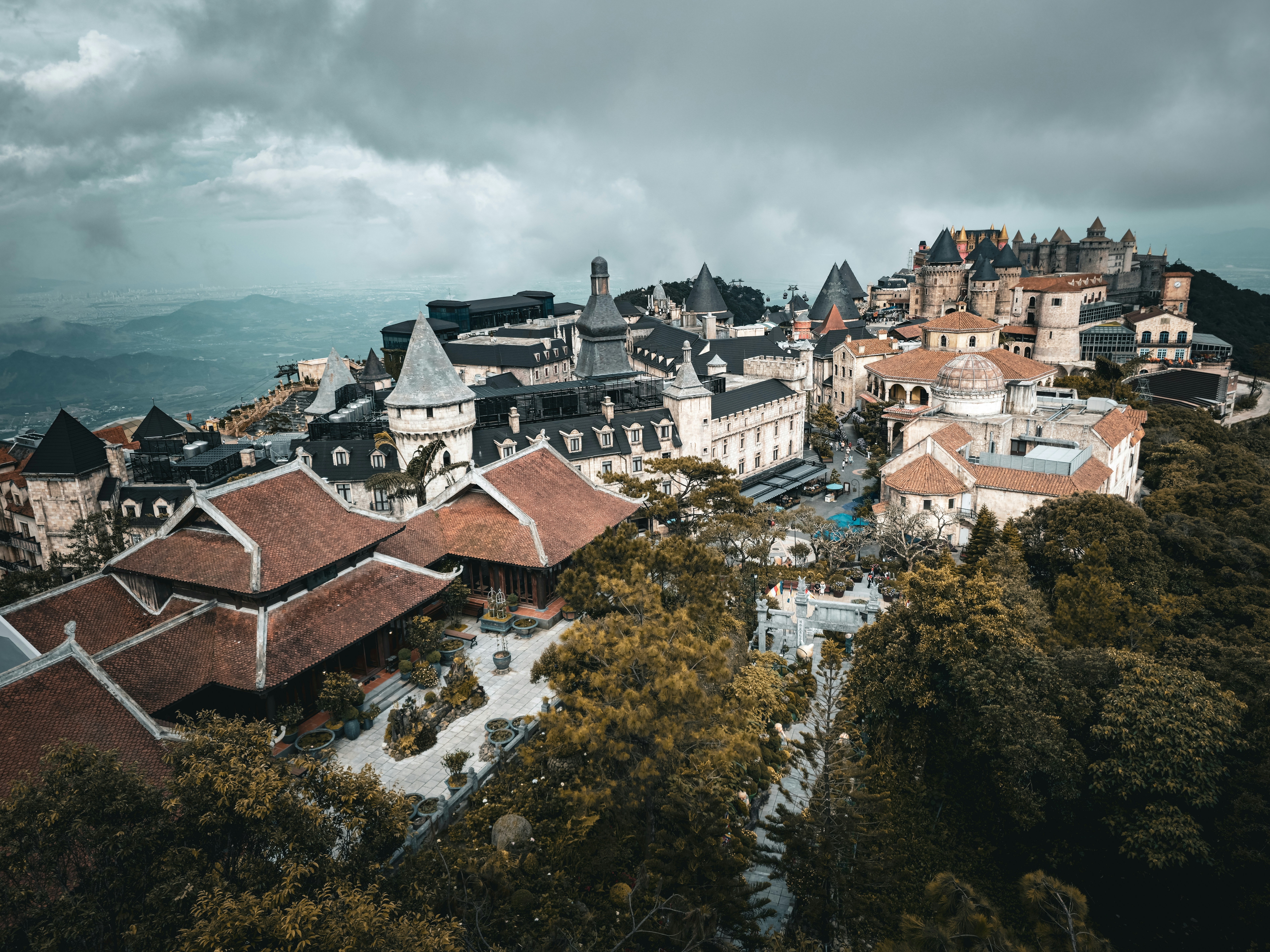 Aerial view of a sprawling resort complex nestled in the mountains, featuring intricate architecture and lush greenery. The scene captures a blend of natural beauty and human craftsmanship.