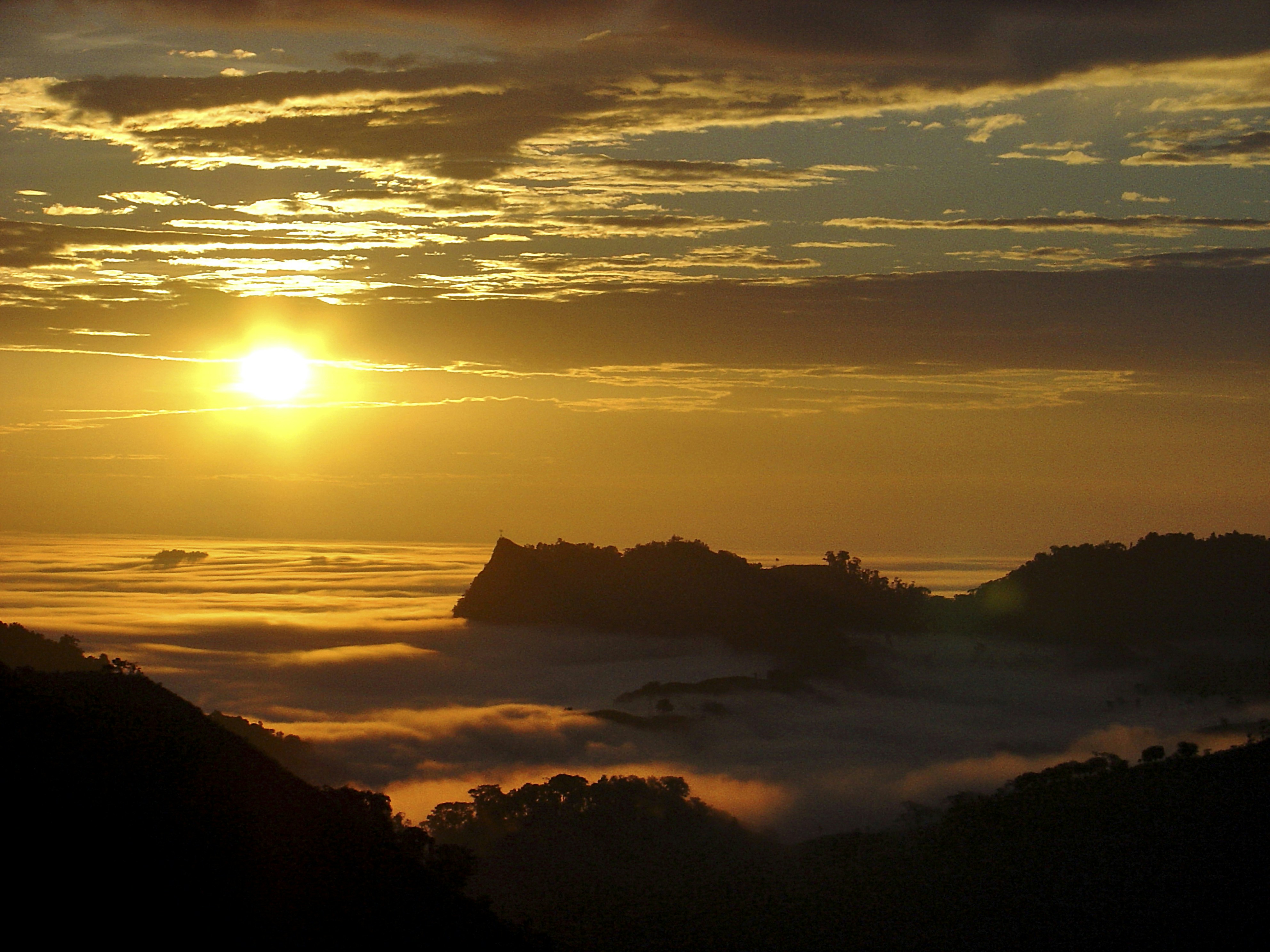 Sunset casting golden hues over silhouetted hills and misty waters.