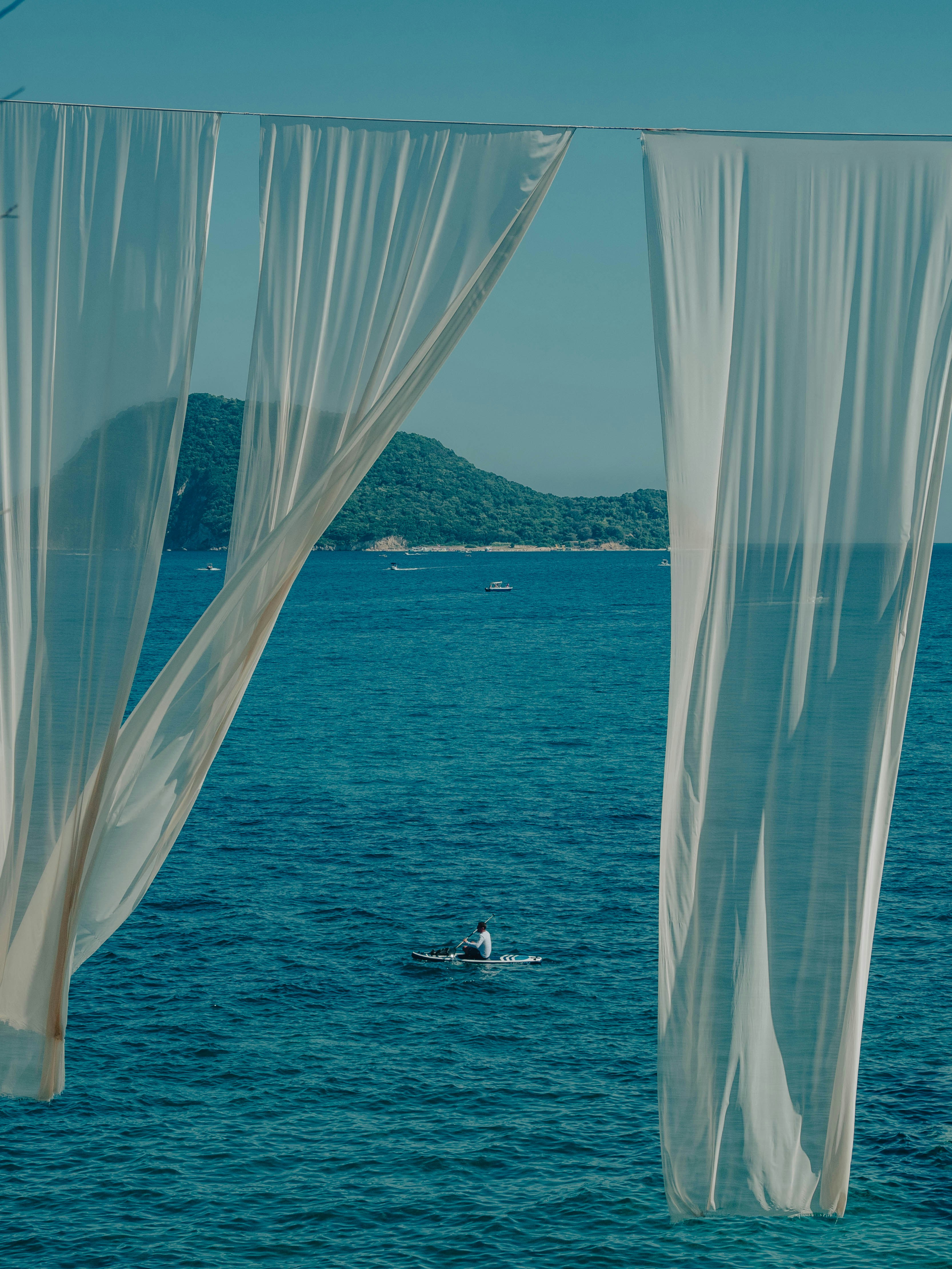 Curtain-Framed Sea: A Lone Boat Meets a Sapphire Horizon
