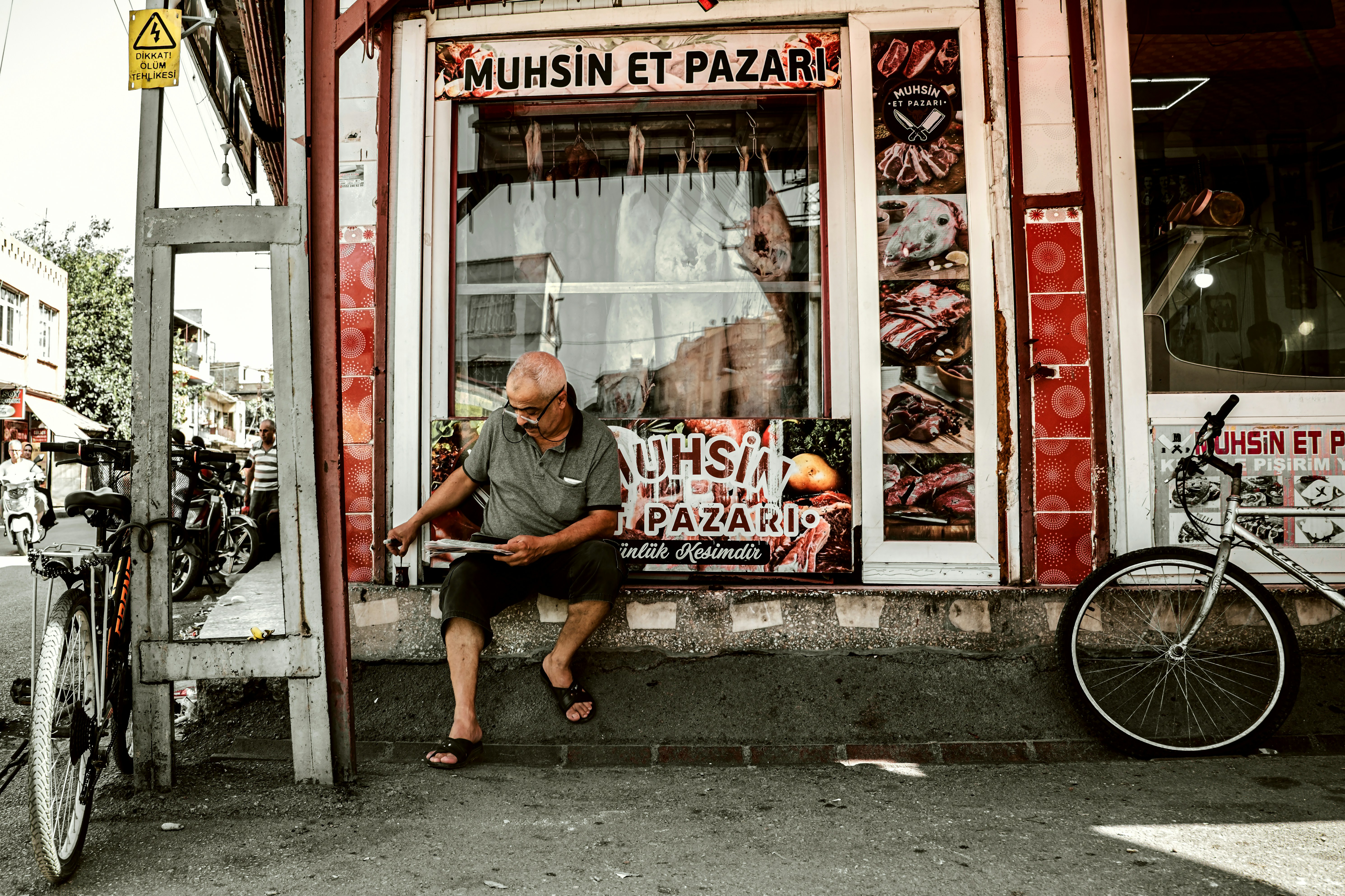 Man sitting outside a butcher shop with bicycles leaning against the storefront.