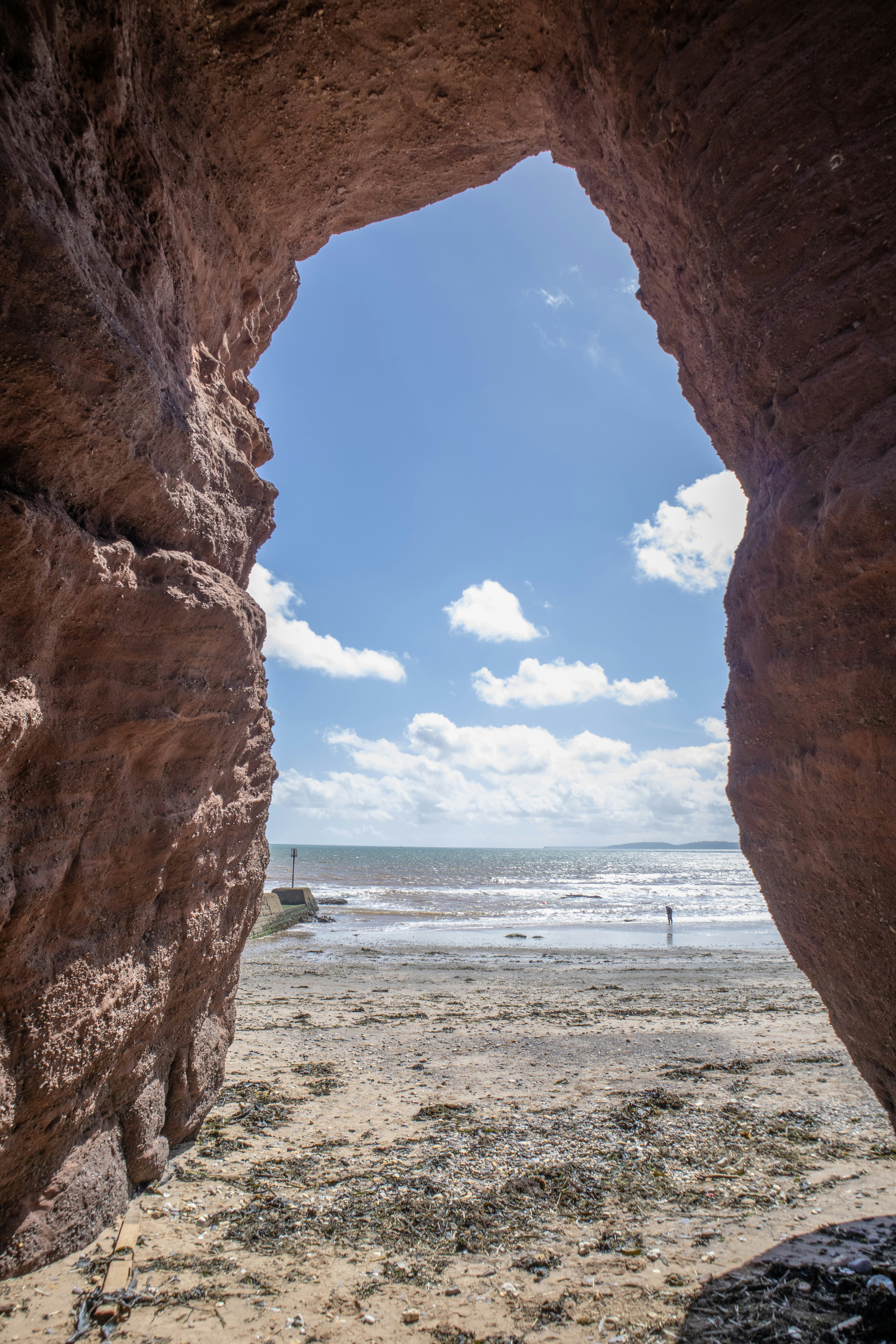 A person standing on a beach under a rock formation photo – Free Beach ...