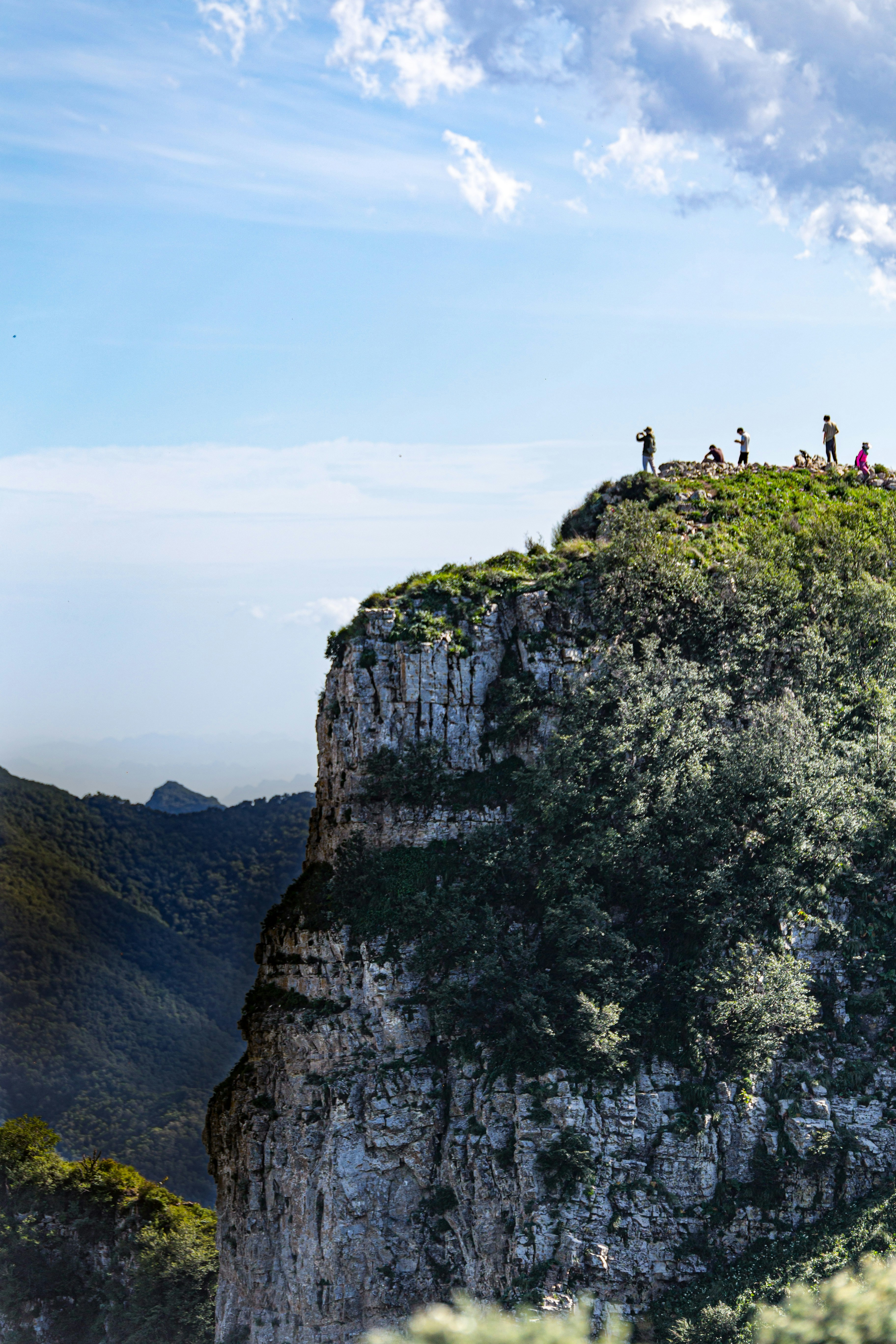Clifftop Assembly: Hikers pausing along a windswept ledge above emerald valleys