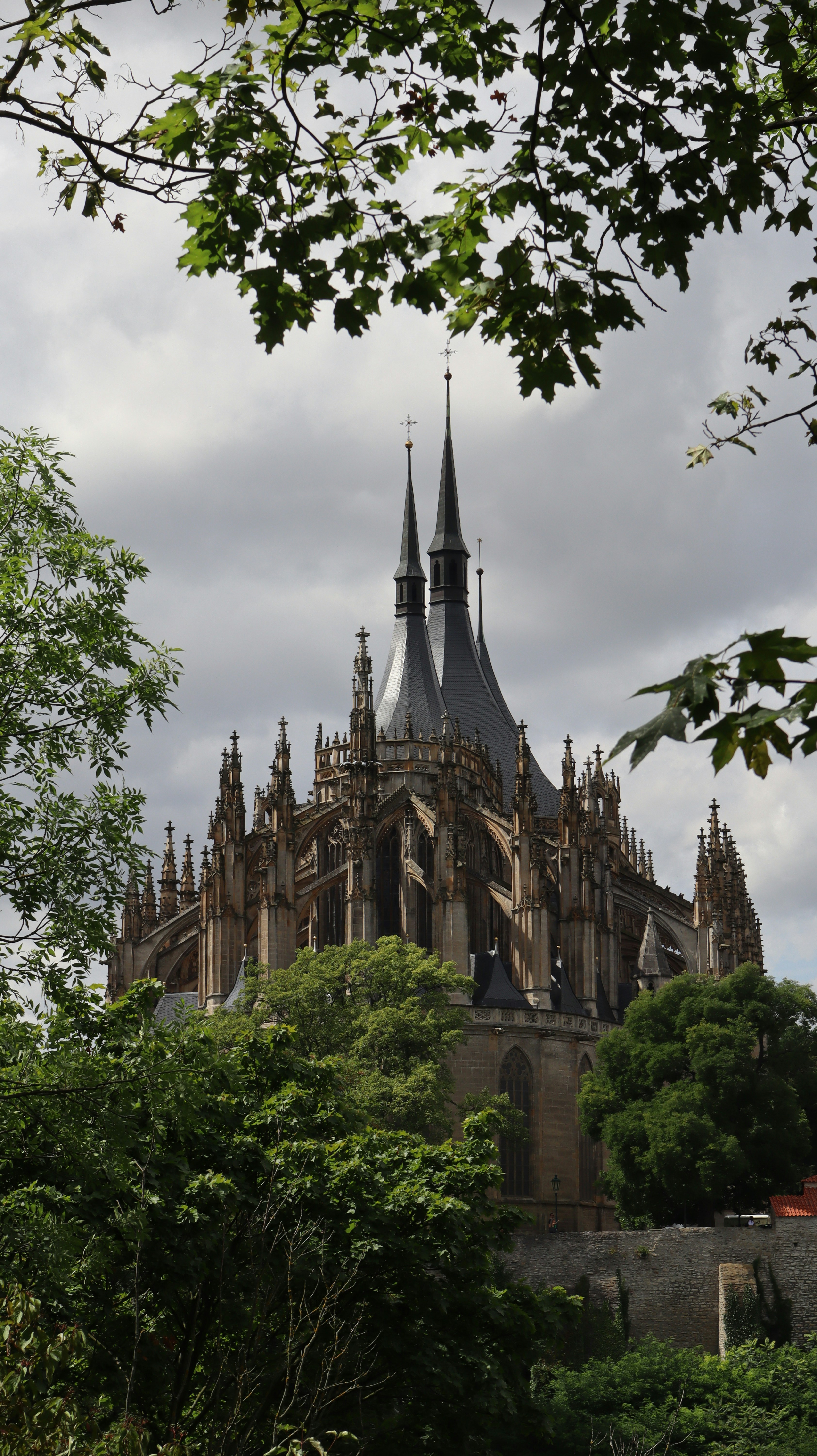 Gothic cathedral with towering spires set against a cloudy sky, framed by lush green foliage.