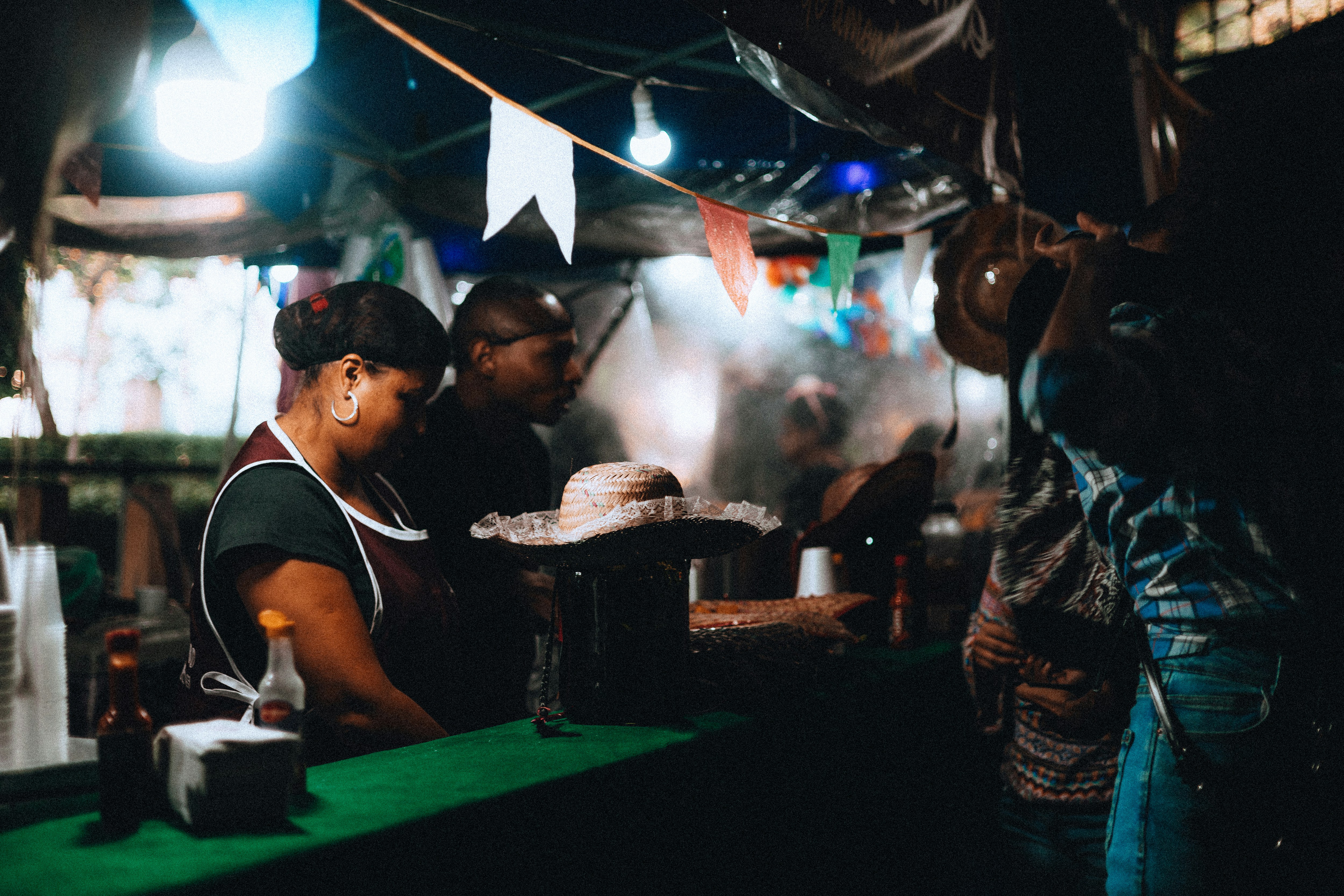 Vendors prepare food under string lights at an outdoor market.