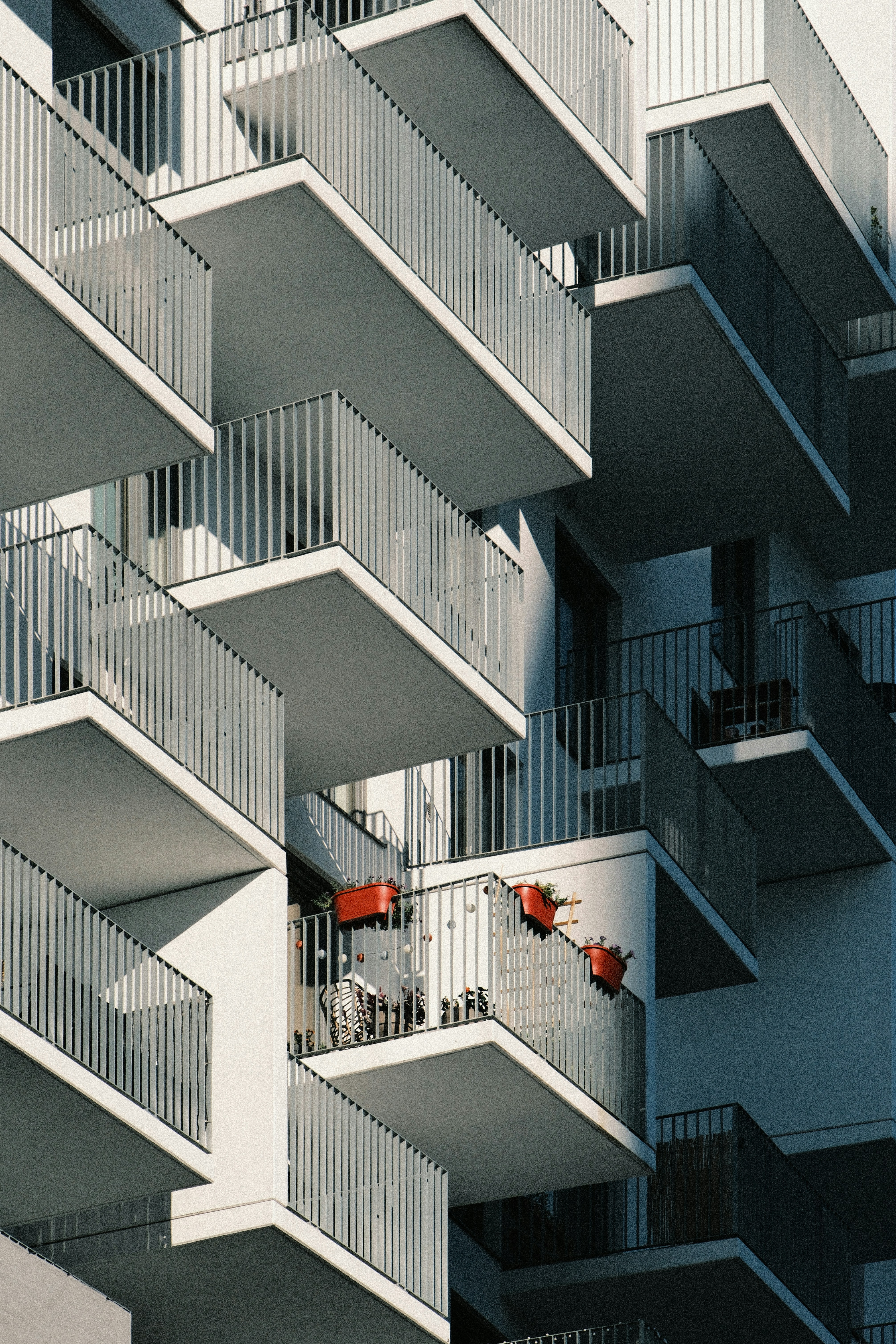 Architectural photograph of stacked balconies forming diagonal planes, with red pots accenting a central terrace.