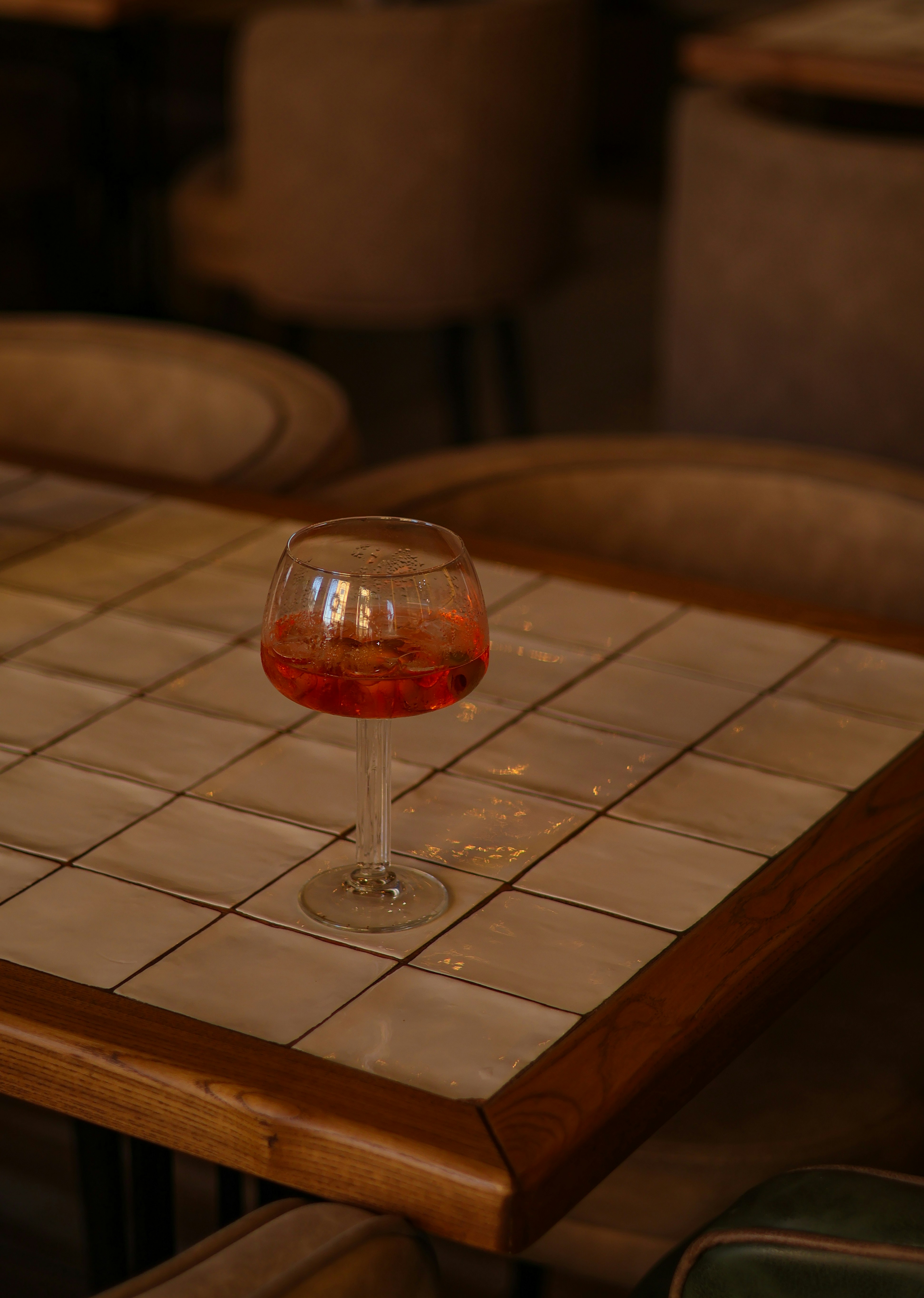 A photograph of a red wine glass on a checkered tile table in a dimly lit lounge.