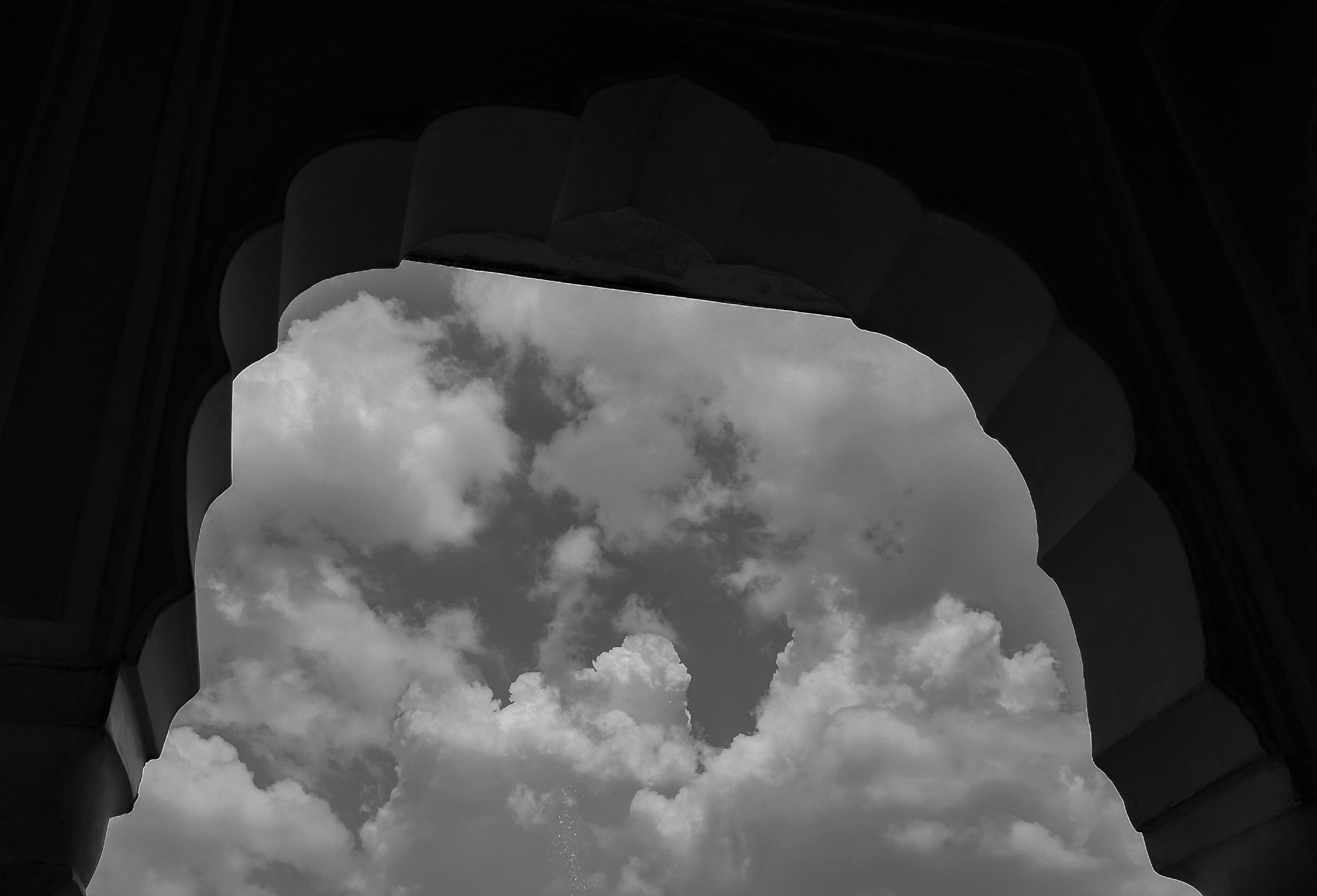 Monochrome archway opening framing a dramatic sky with clouds; architectural silhouette against the pale sky, emphasizing shape over color.