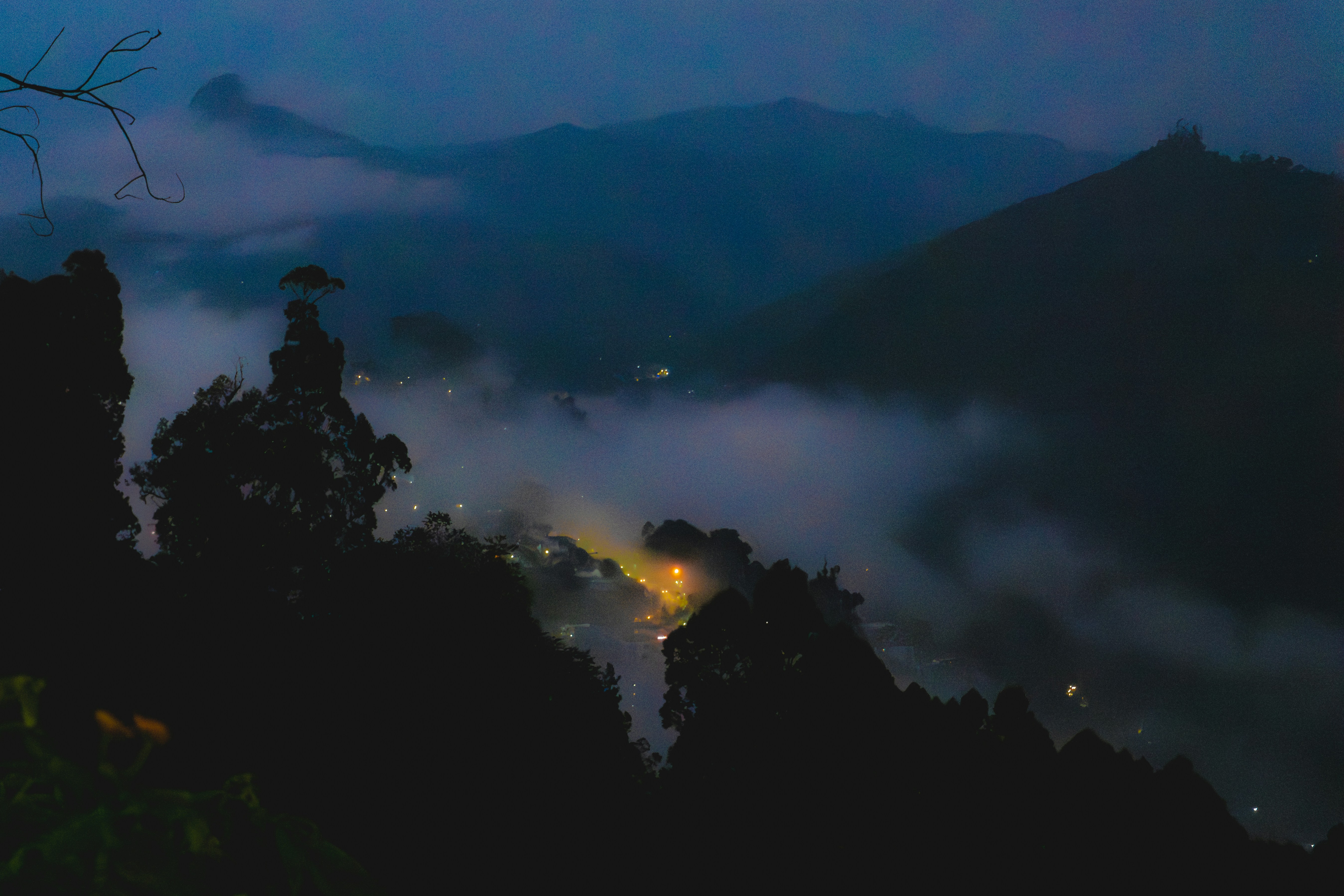 a foggy night in the mountains with a view of a town