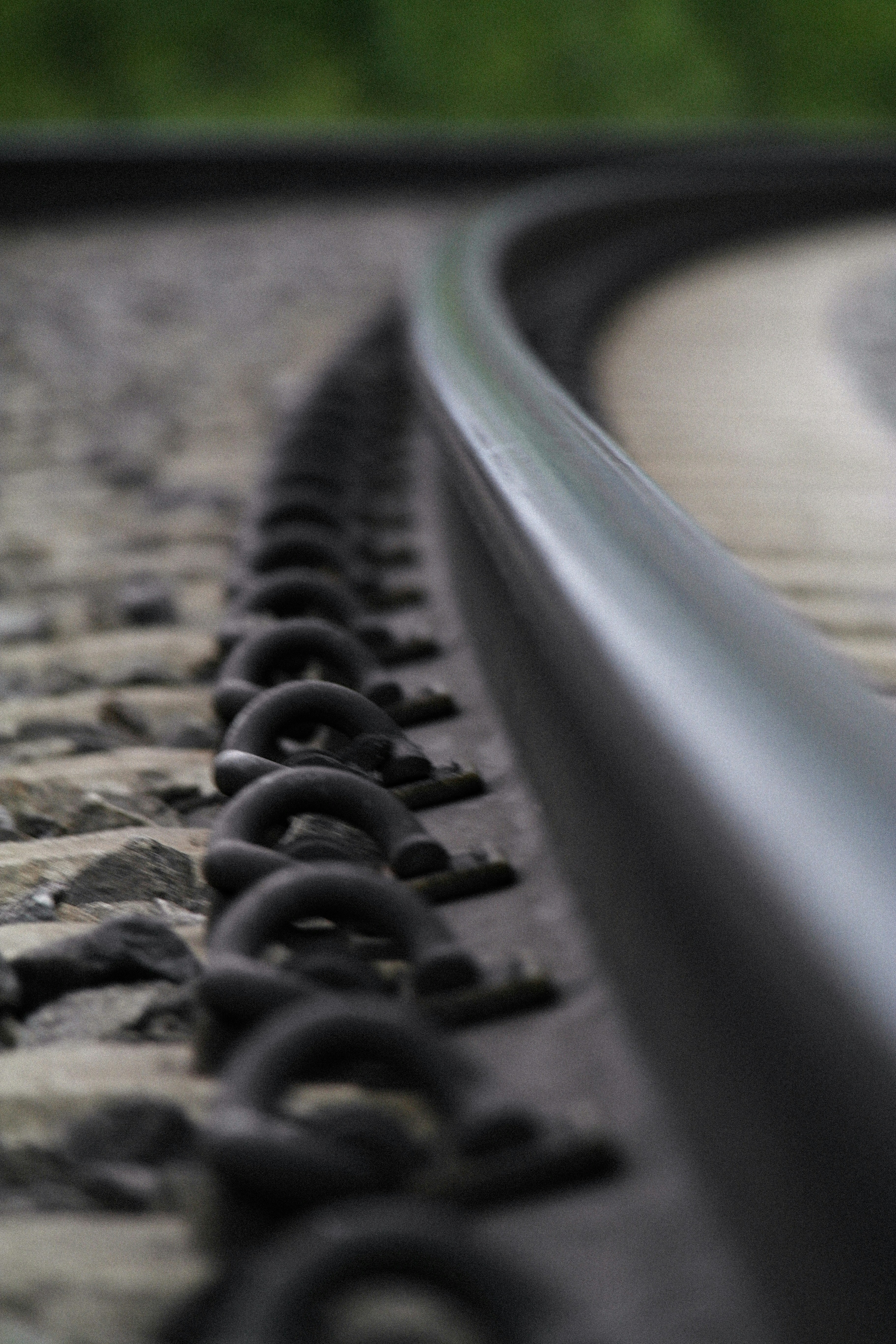 Close-up photograph of a steel railroad rail curving into the distance, with a row of circular tie-like rings set in the ballast. The shallow depth of field emphasizes the rail and near rings.