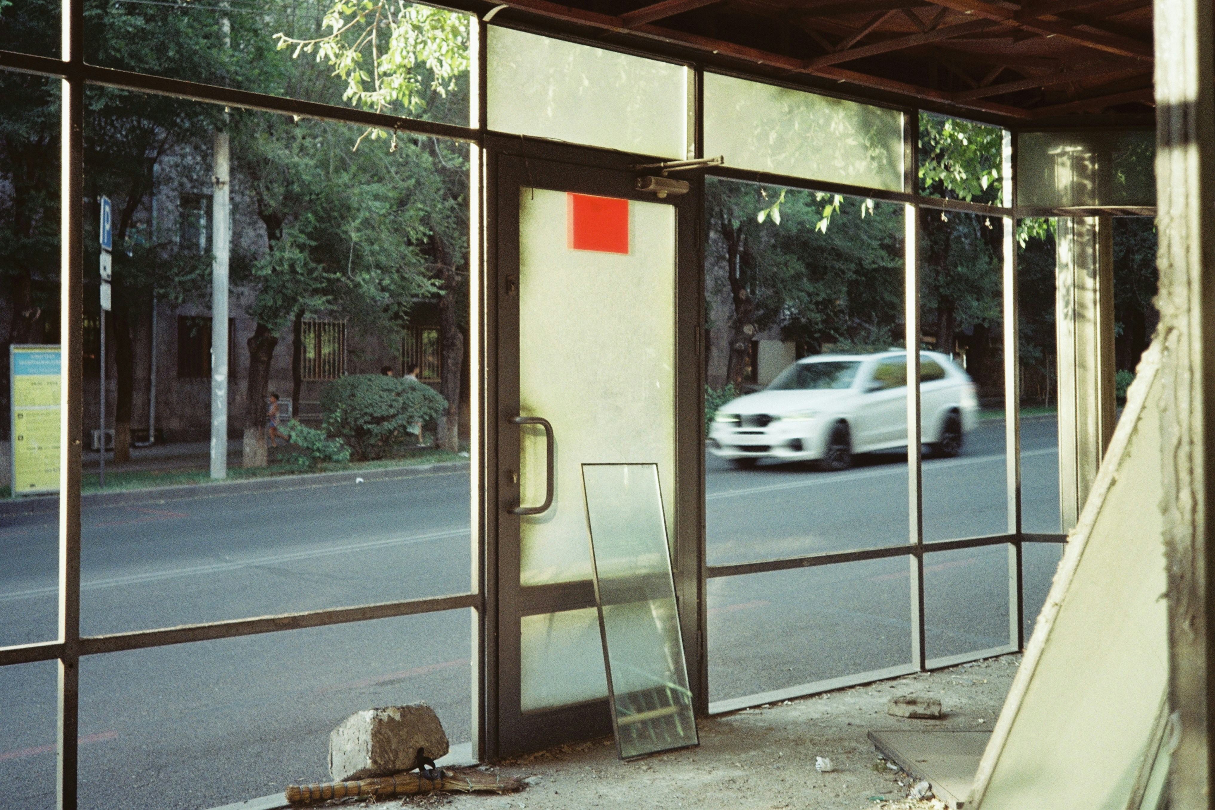 Red Accent in a Glass Bus Shelter as a Car Blurs Past