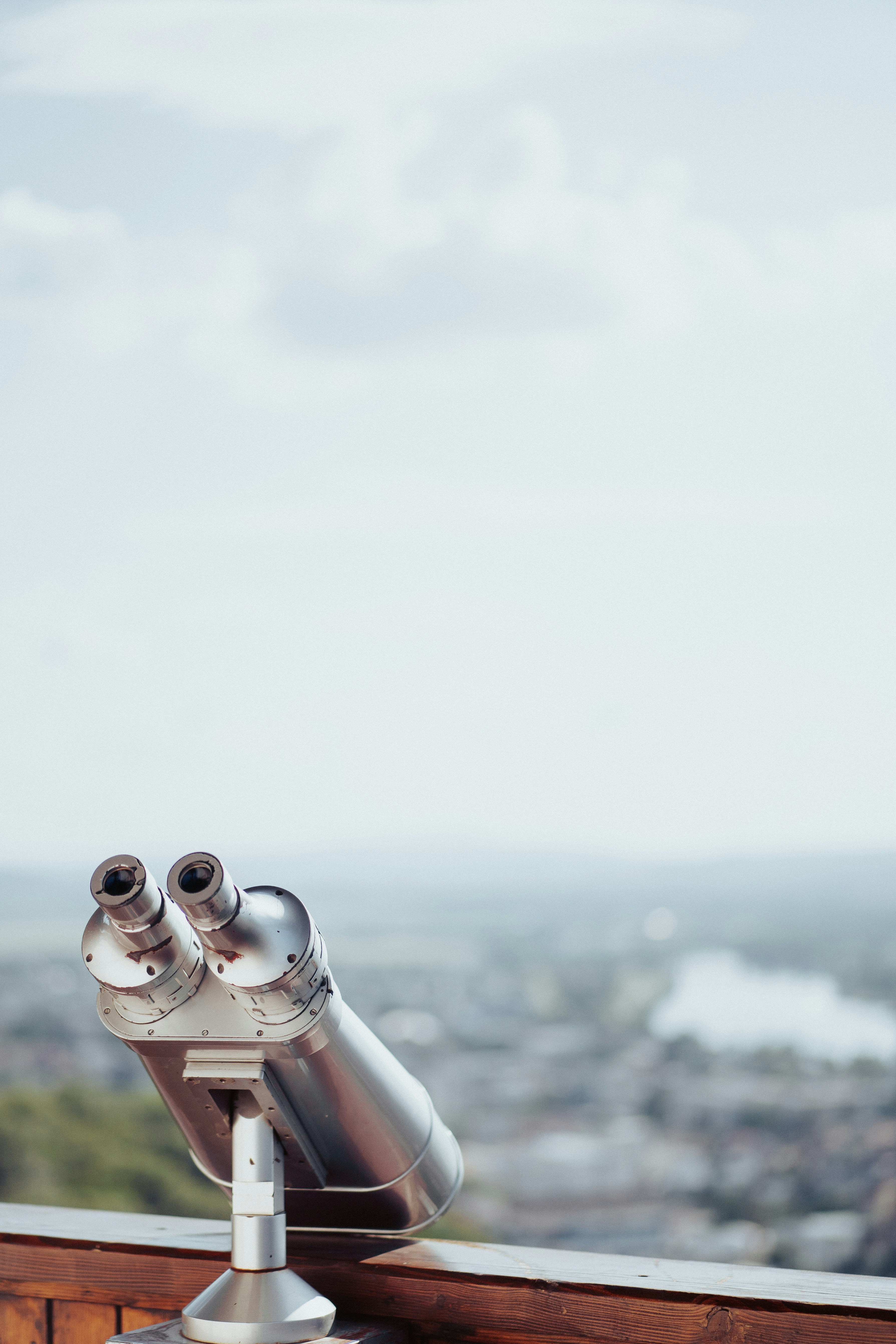 Twin-barrel viewing telescope perched on a wooden railing overlooking a hazy river valley