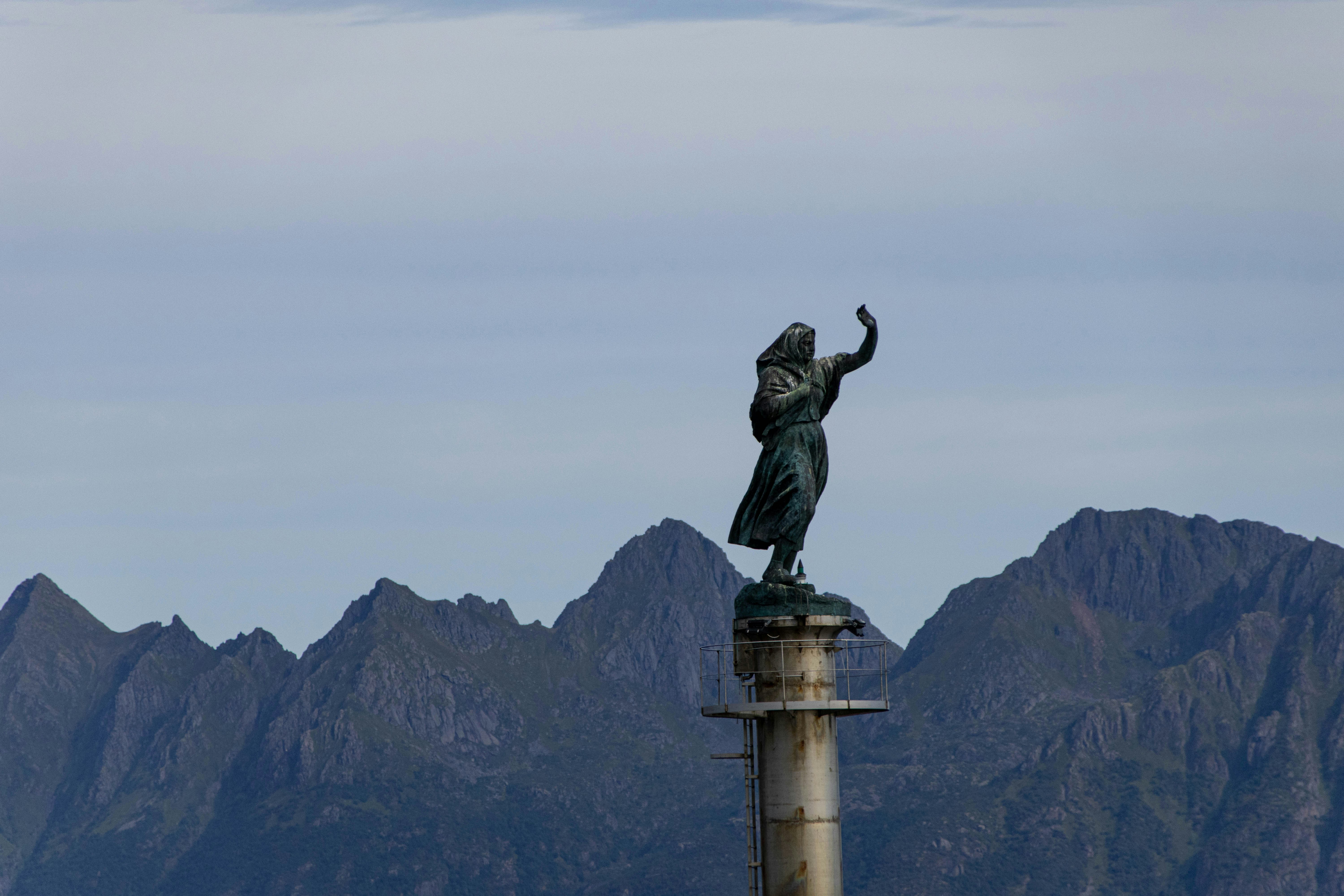 Alpine Sentinel: Bronze Figure on a Pillar Over the Jagged Peaks