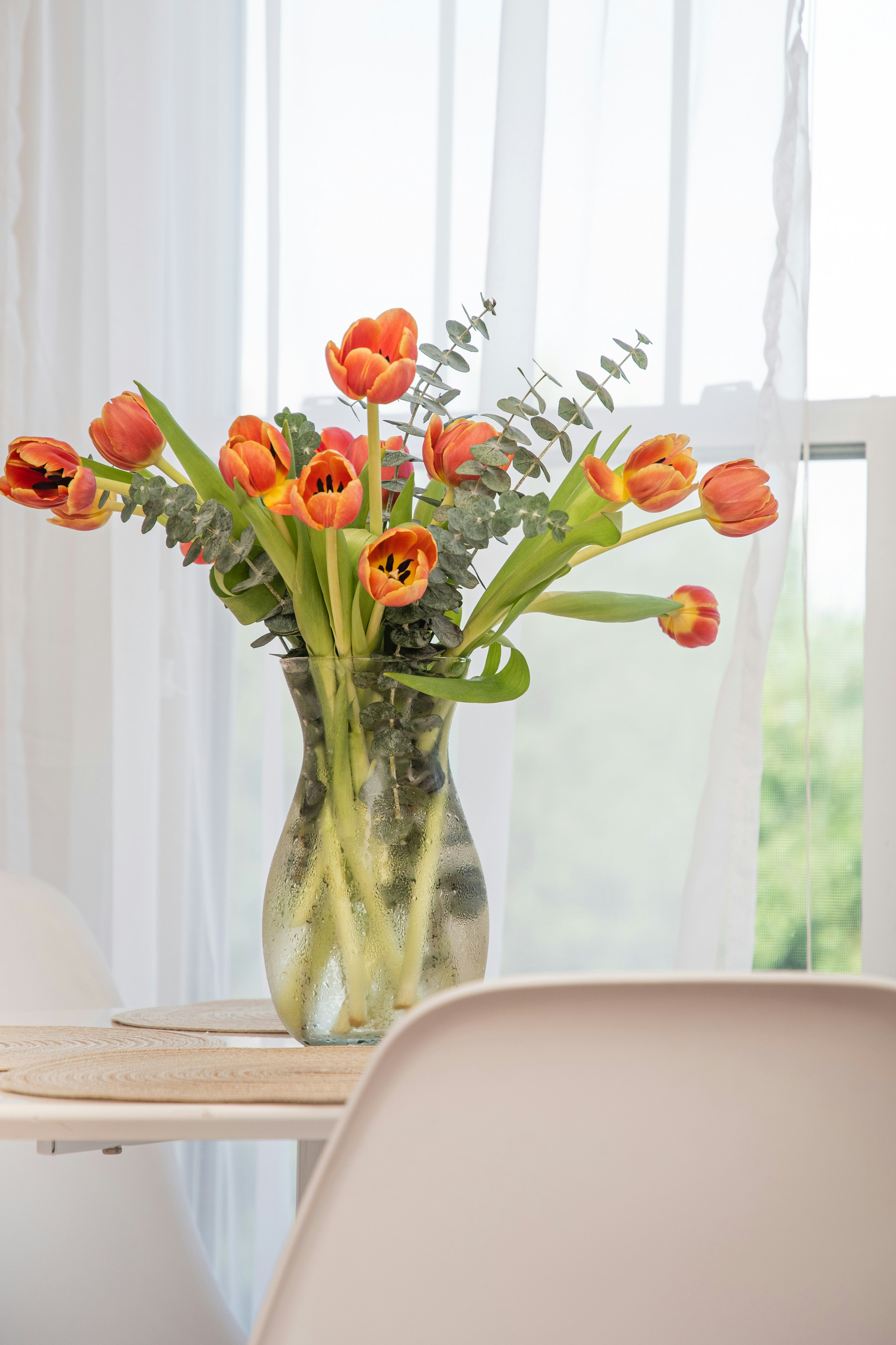 This arrangement tulip flowers placed atop a small white round table, inspiring a minimalist style and evoking feelings of calmness, cleanliness, and simplicity.