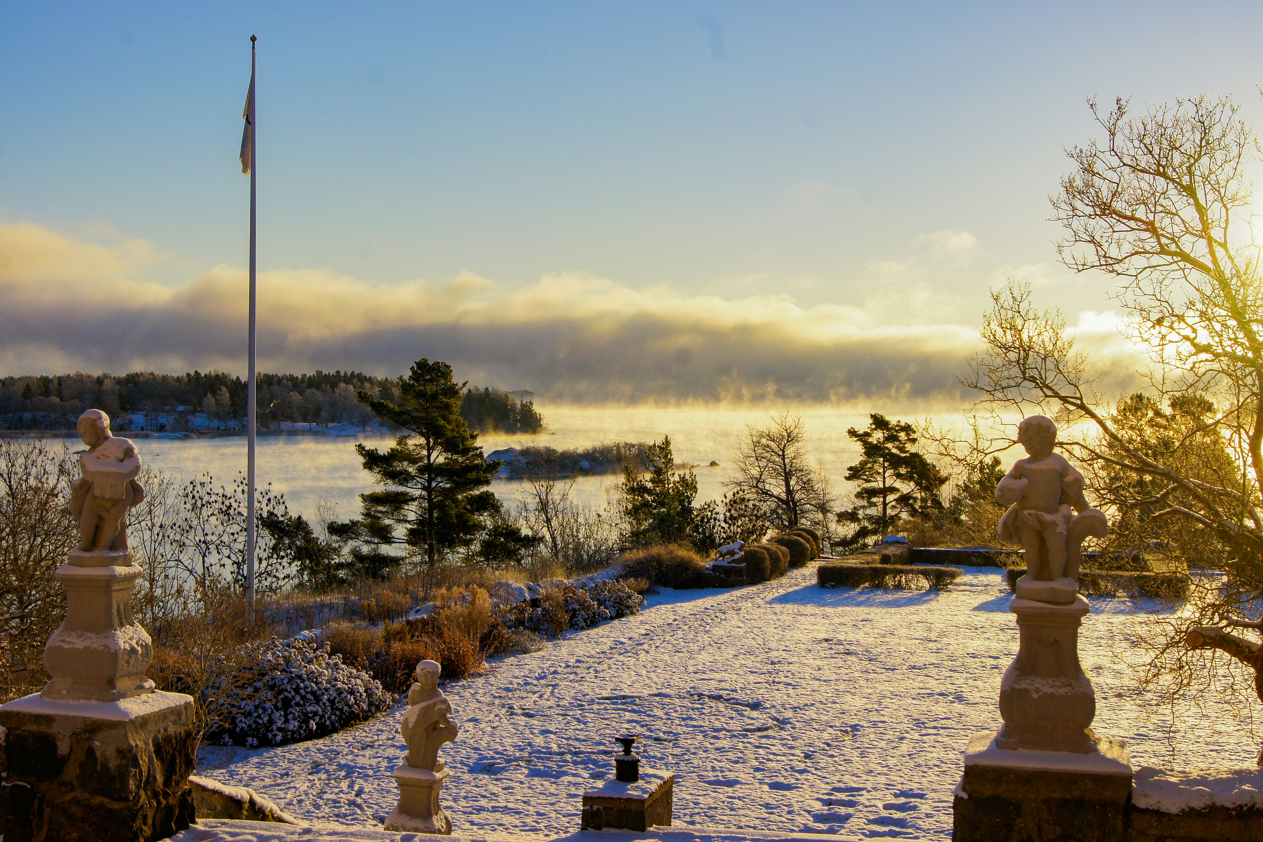 A snow covered walkway with statues and a flag pole photo – Free ...