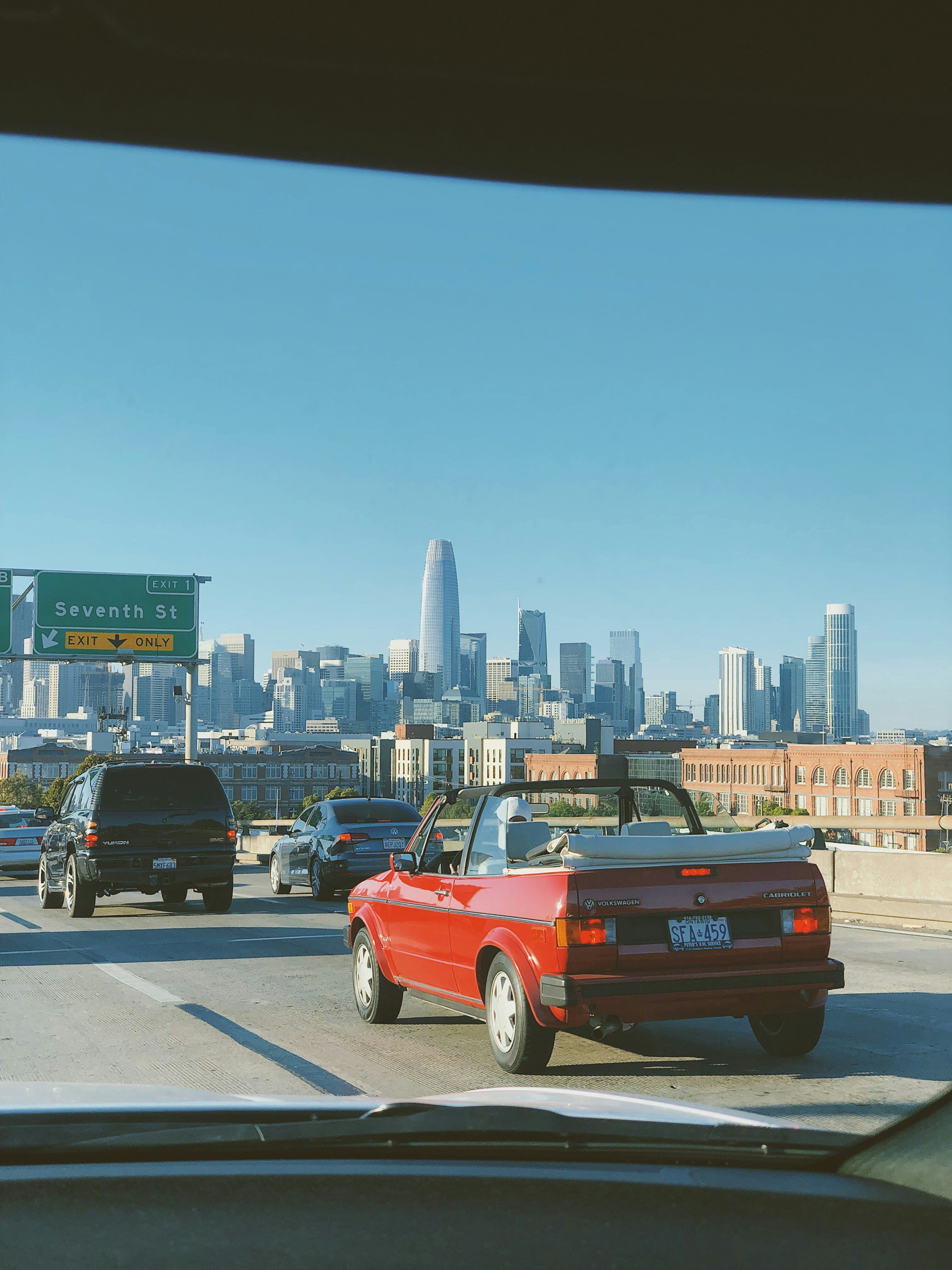 Red Convertible on a Sunlit Freeway with a Distant Downtown Skyline