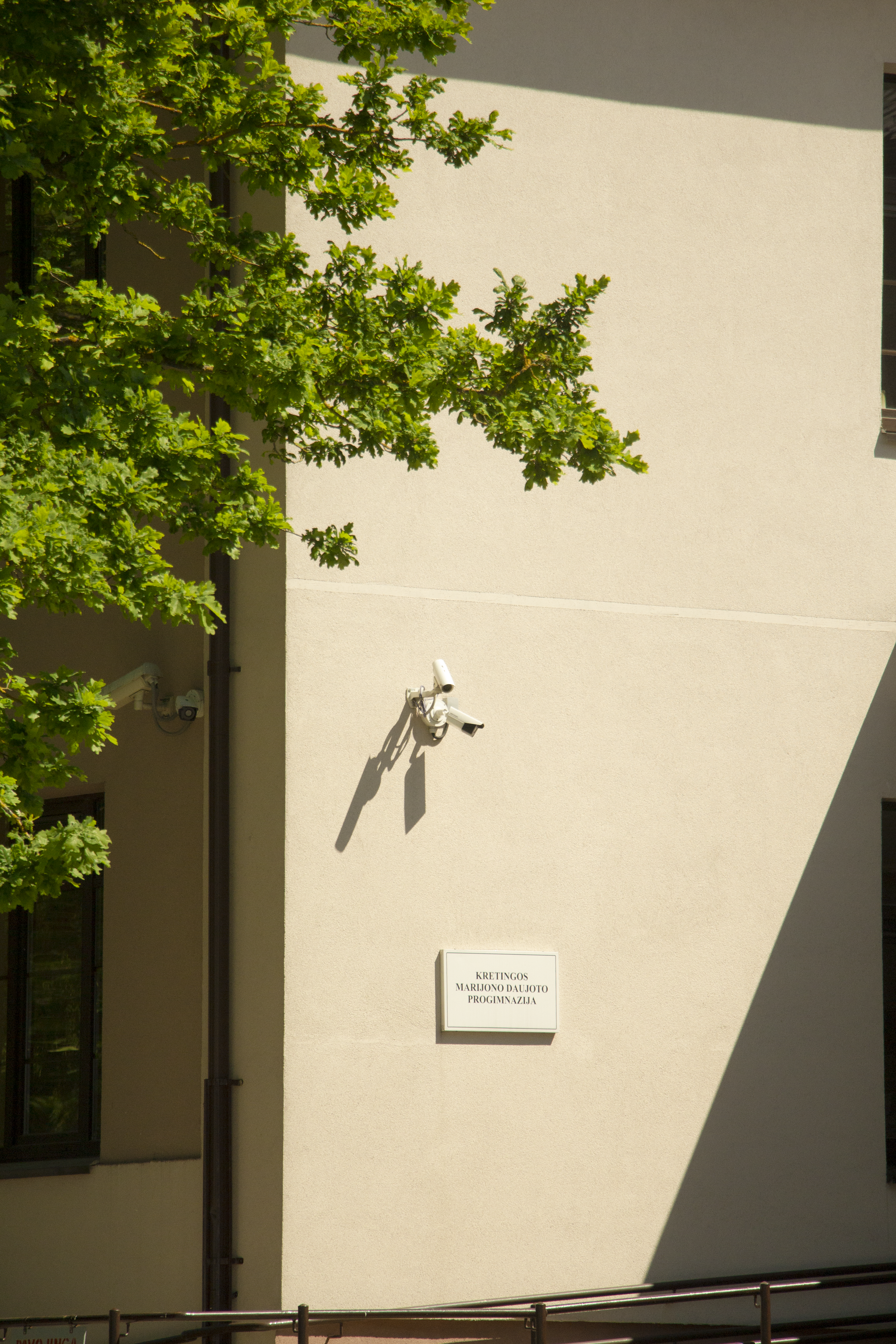 Beige Facade, Watchful Eye: A Security Camera under Dappled Light