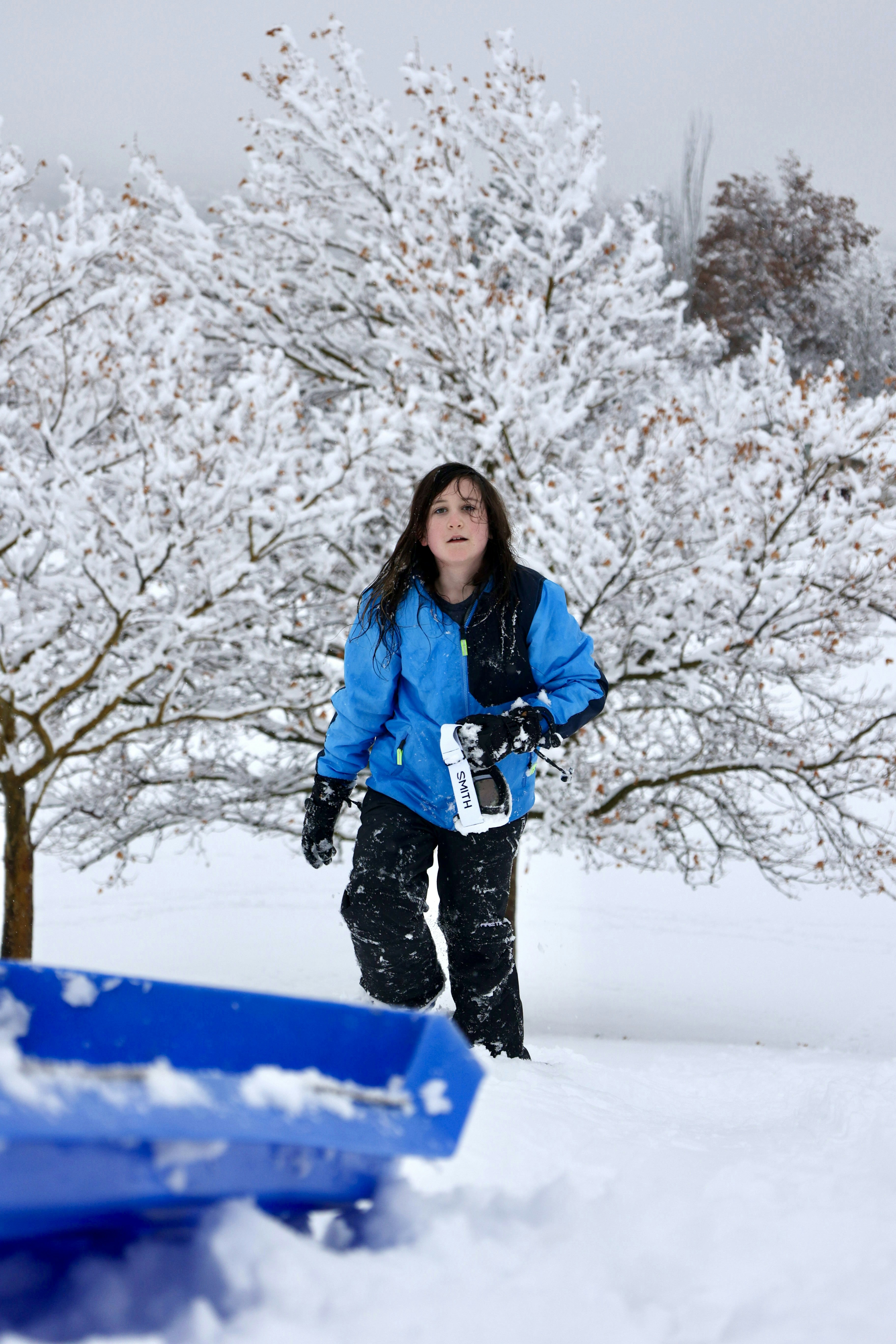 Blue Jacket Sprint Through a Snowbound Orchard Beside a Neon Blue Sled