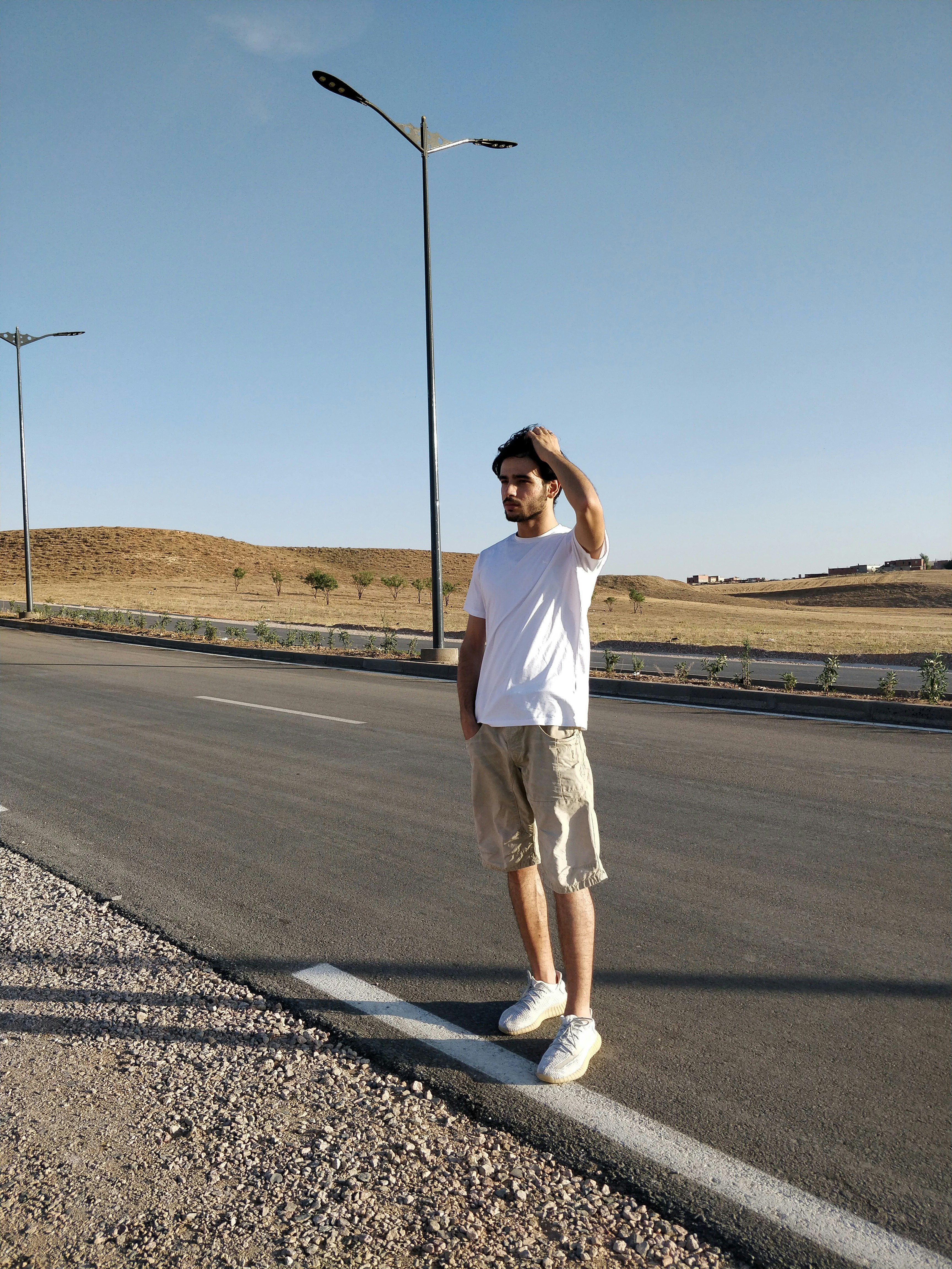Solitary Wanderer on a Sunlit Desert Road with Twin Lamp Posts