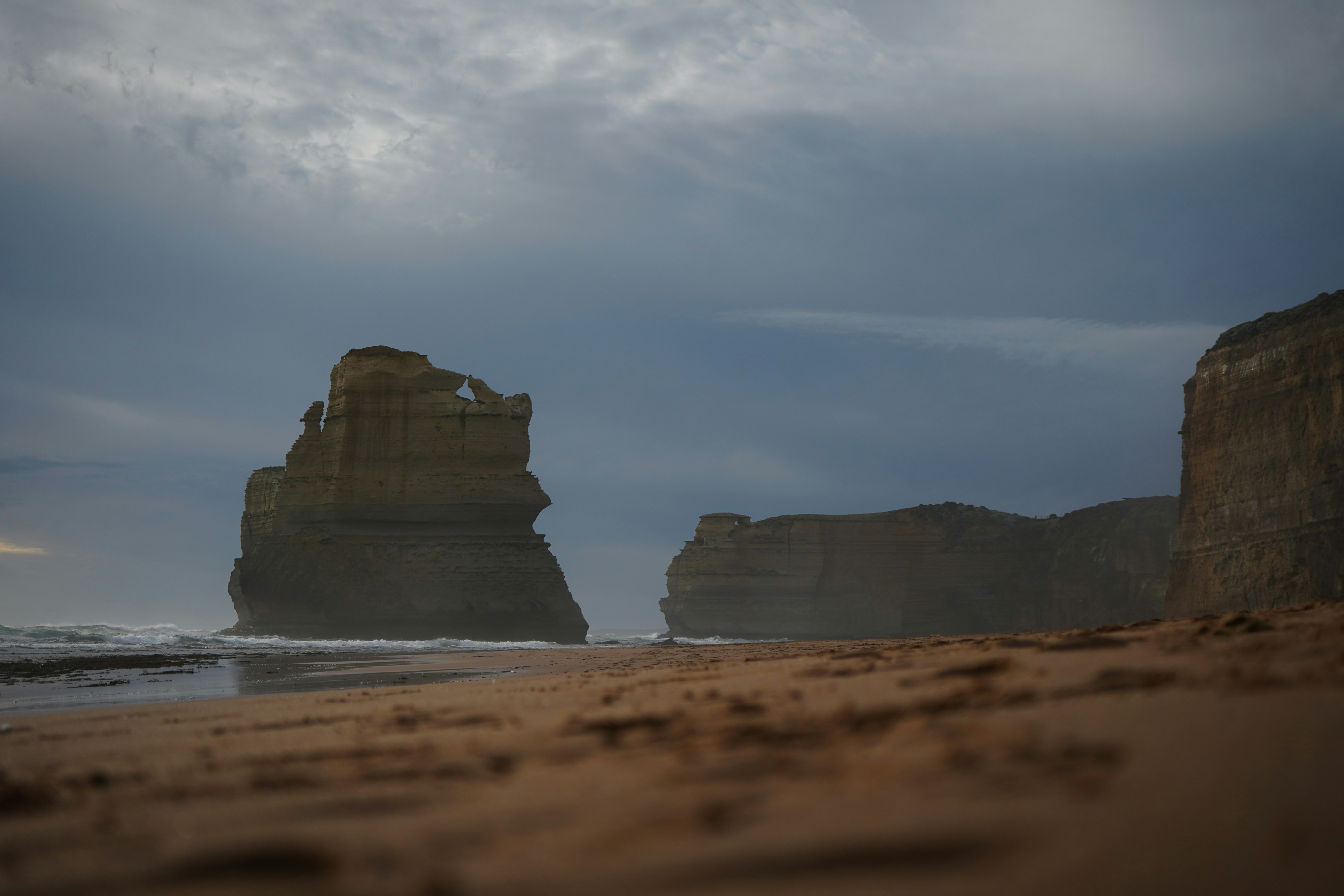 Majestic rock formations rise from the sandy beach under a moody sky, capturing the essence of nature's artistry.