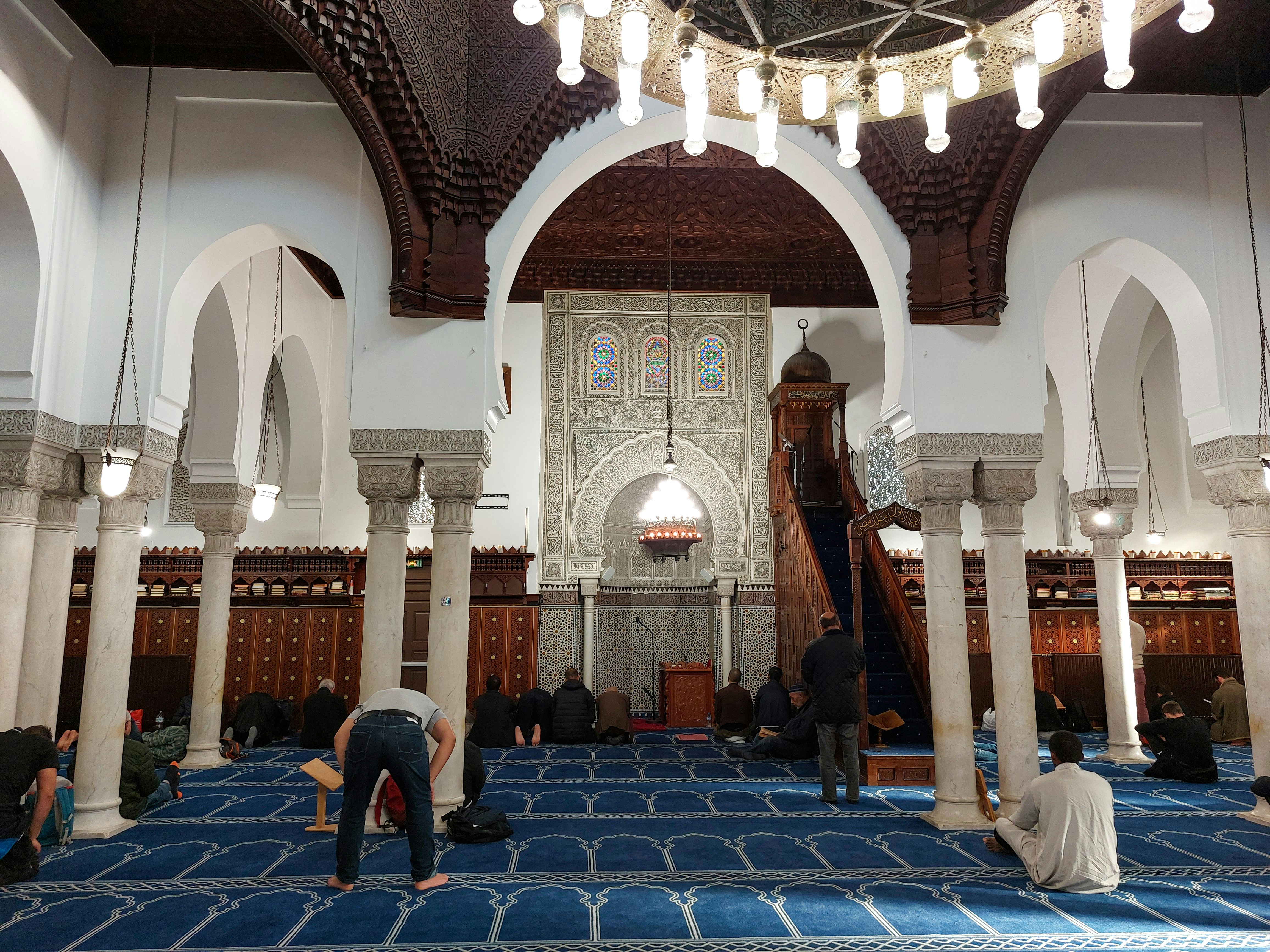 People engaged in prayer within a grand mosque adorned with intricate arches and a blue carpet.