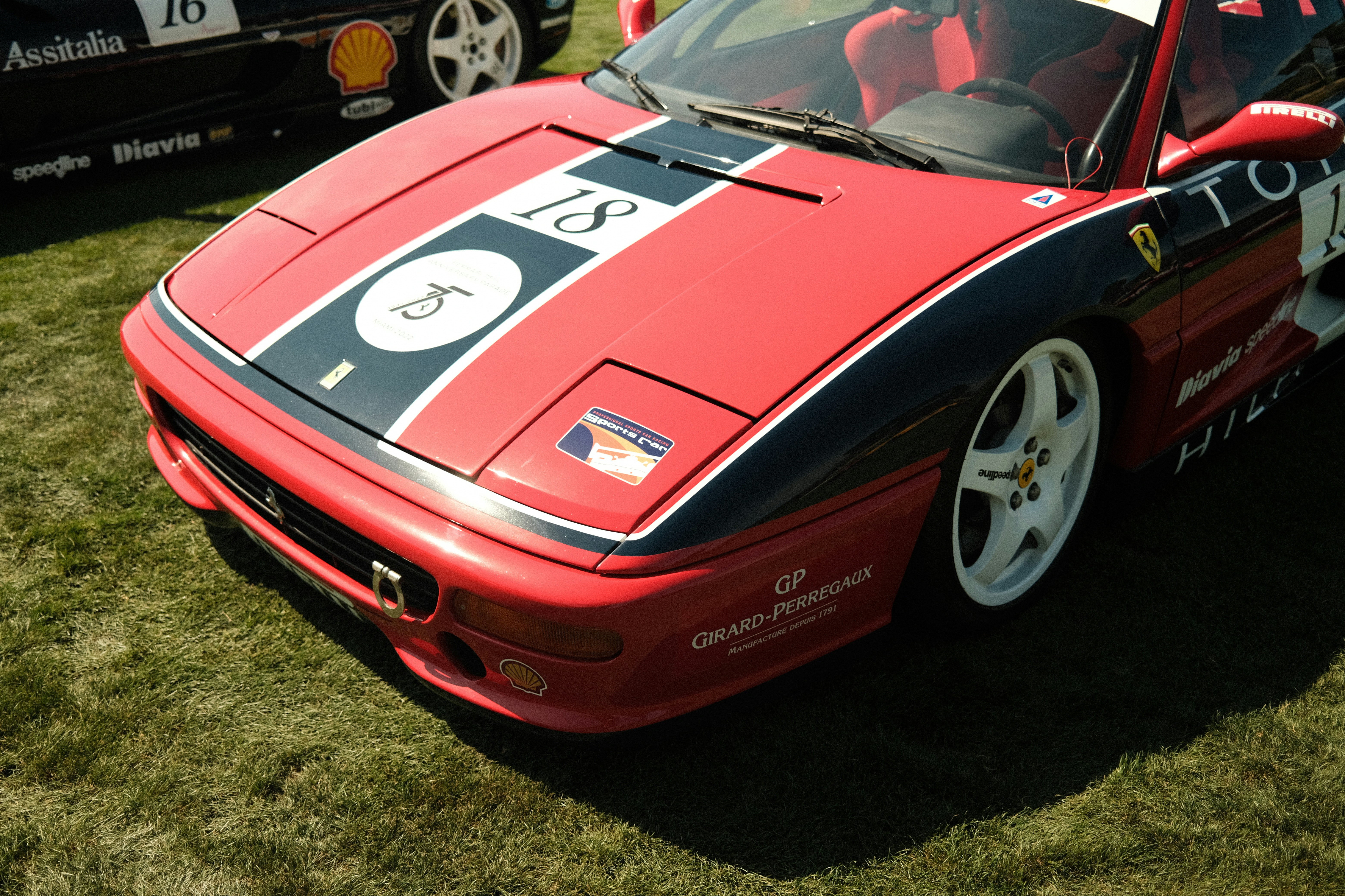 Scarlet Ferrari race car with hood number 18 on a sunlit grass field