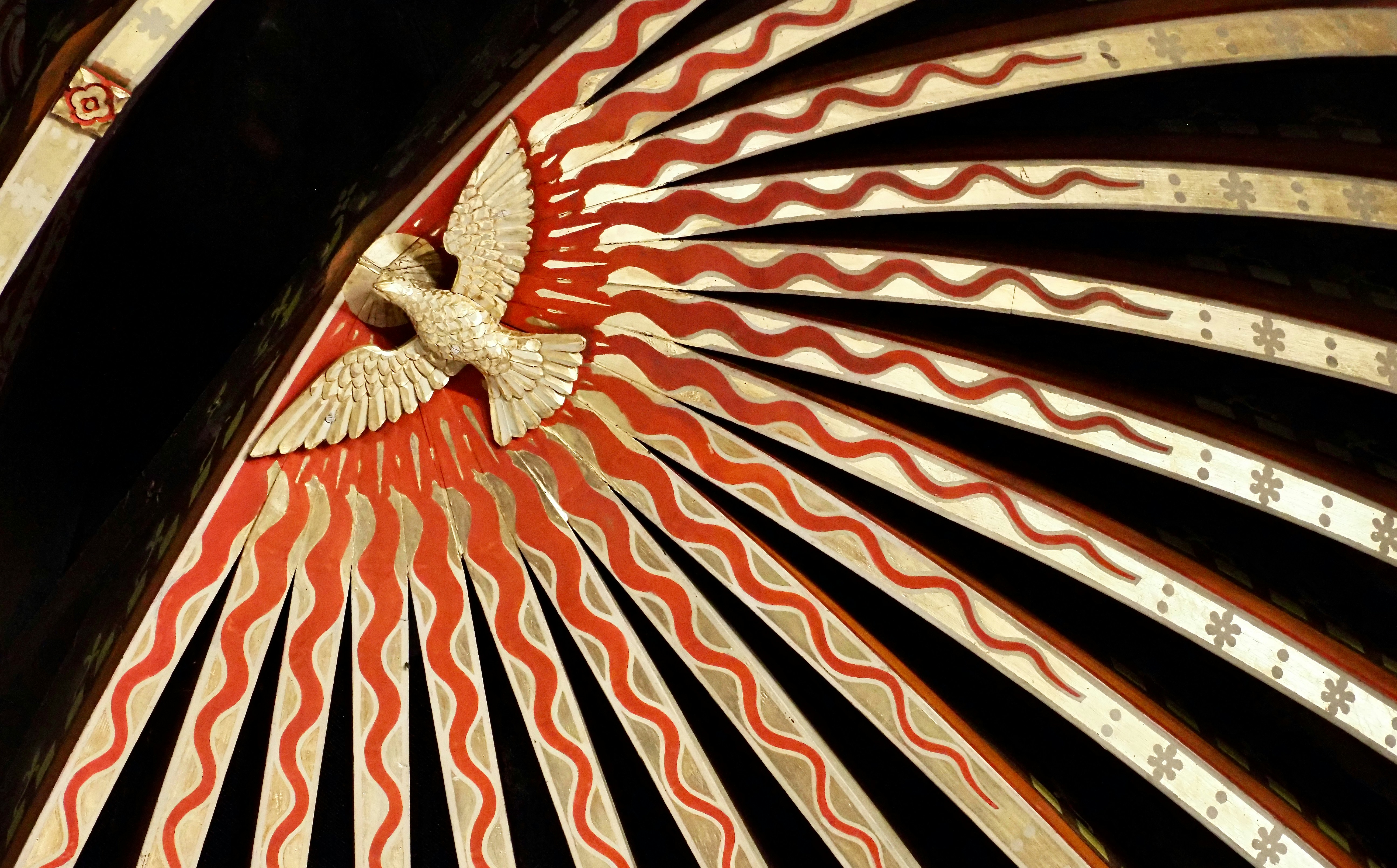 Artistic chancel roof with a white dove and radiating red and gold patterns.