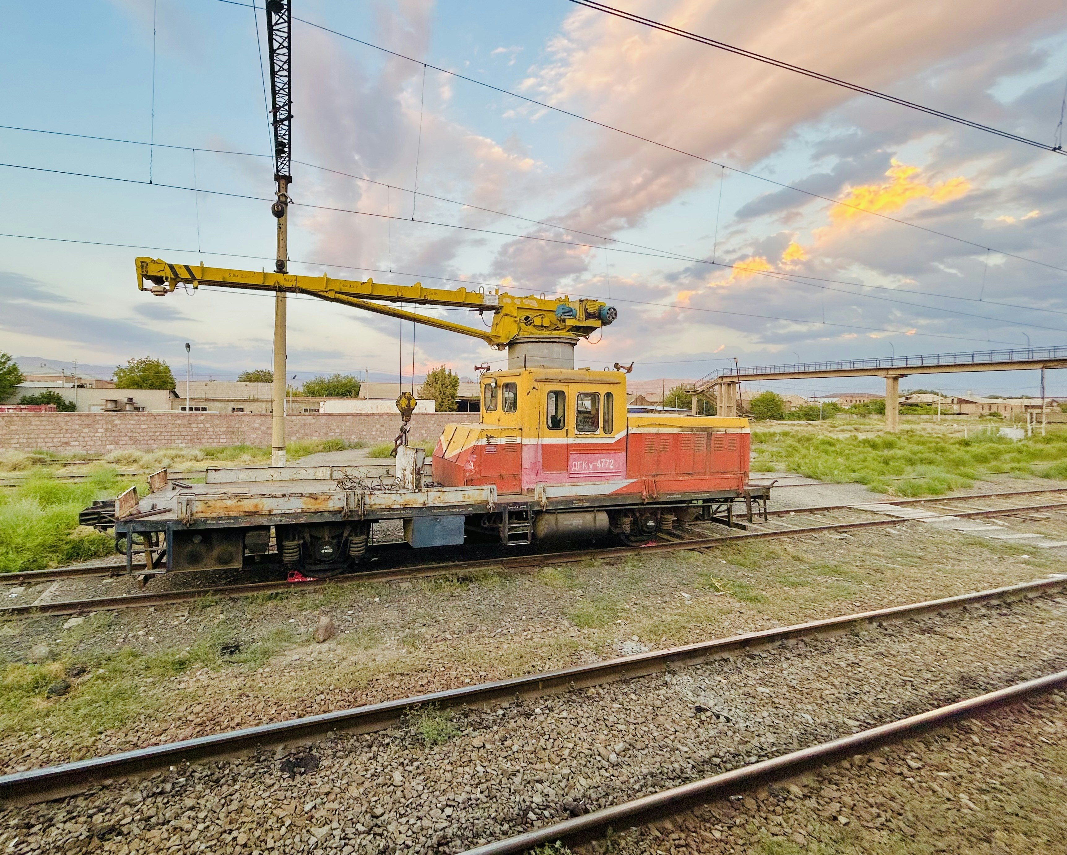 Yellow crane on weathered railcar under a pastel sky