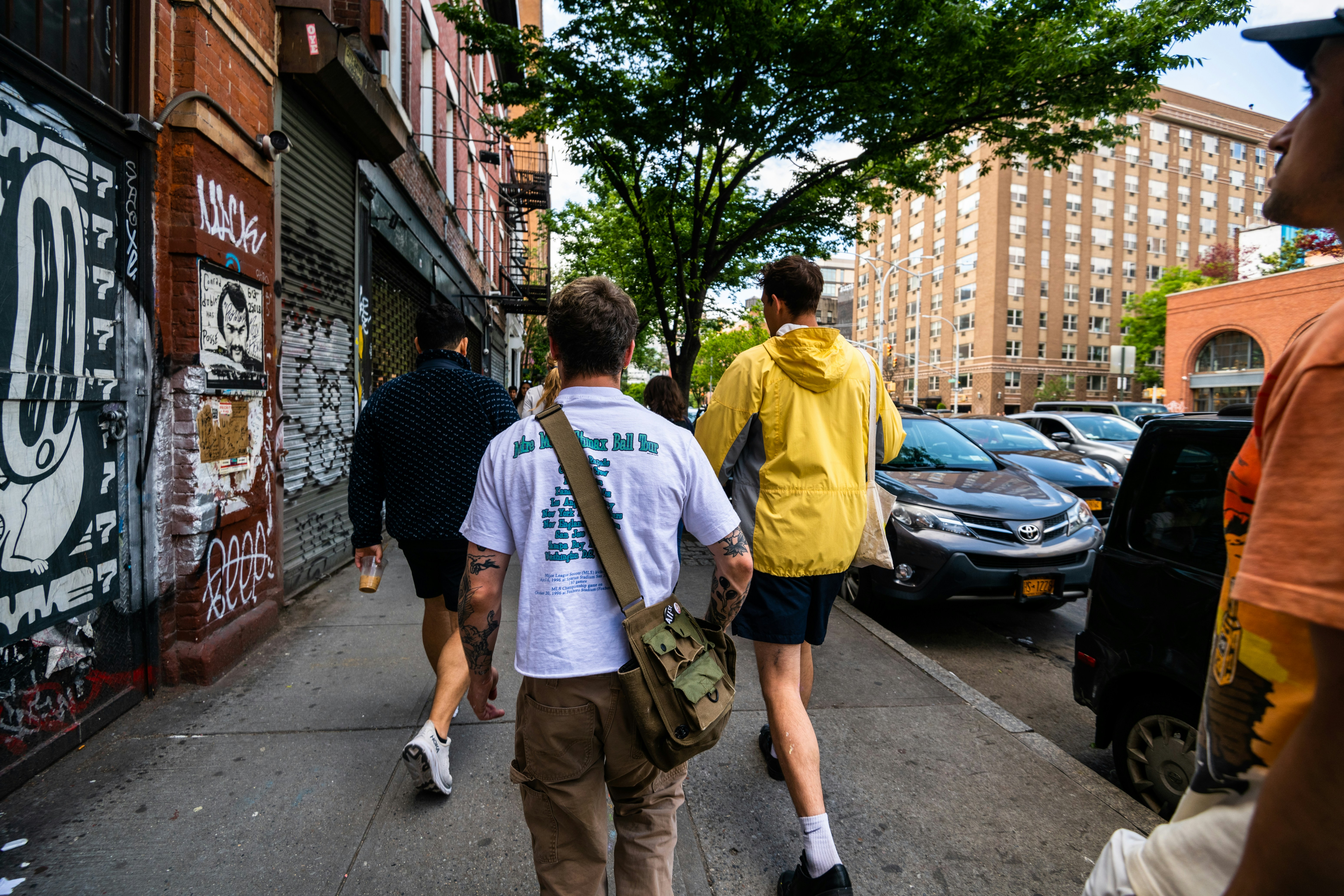 Urban Crossing: Yellow-hooded stride leads a small group along a graffiti-streaked sidewalk