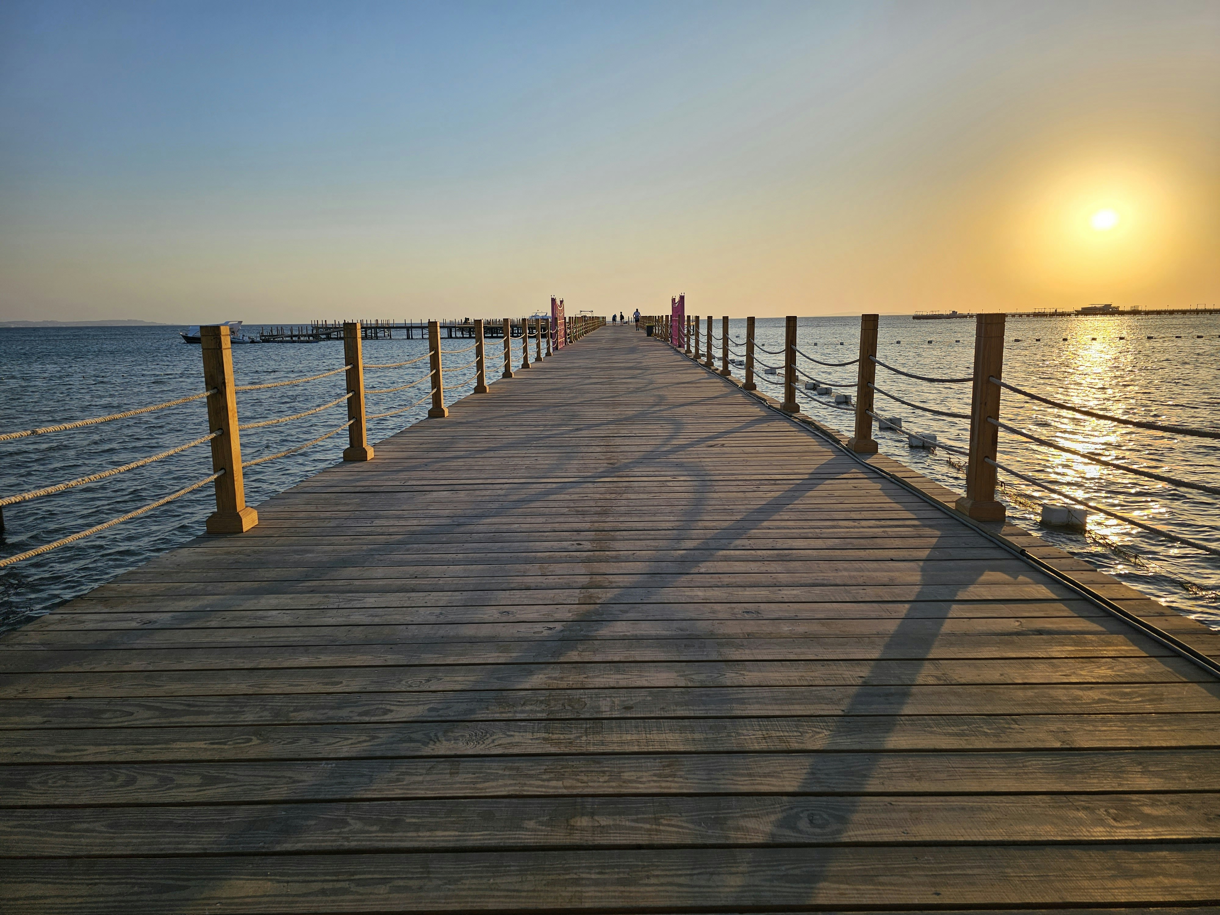 Wooden pier extending into the shimmering water, framed by a setting sun casting golden hues across the scene.
