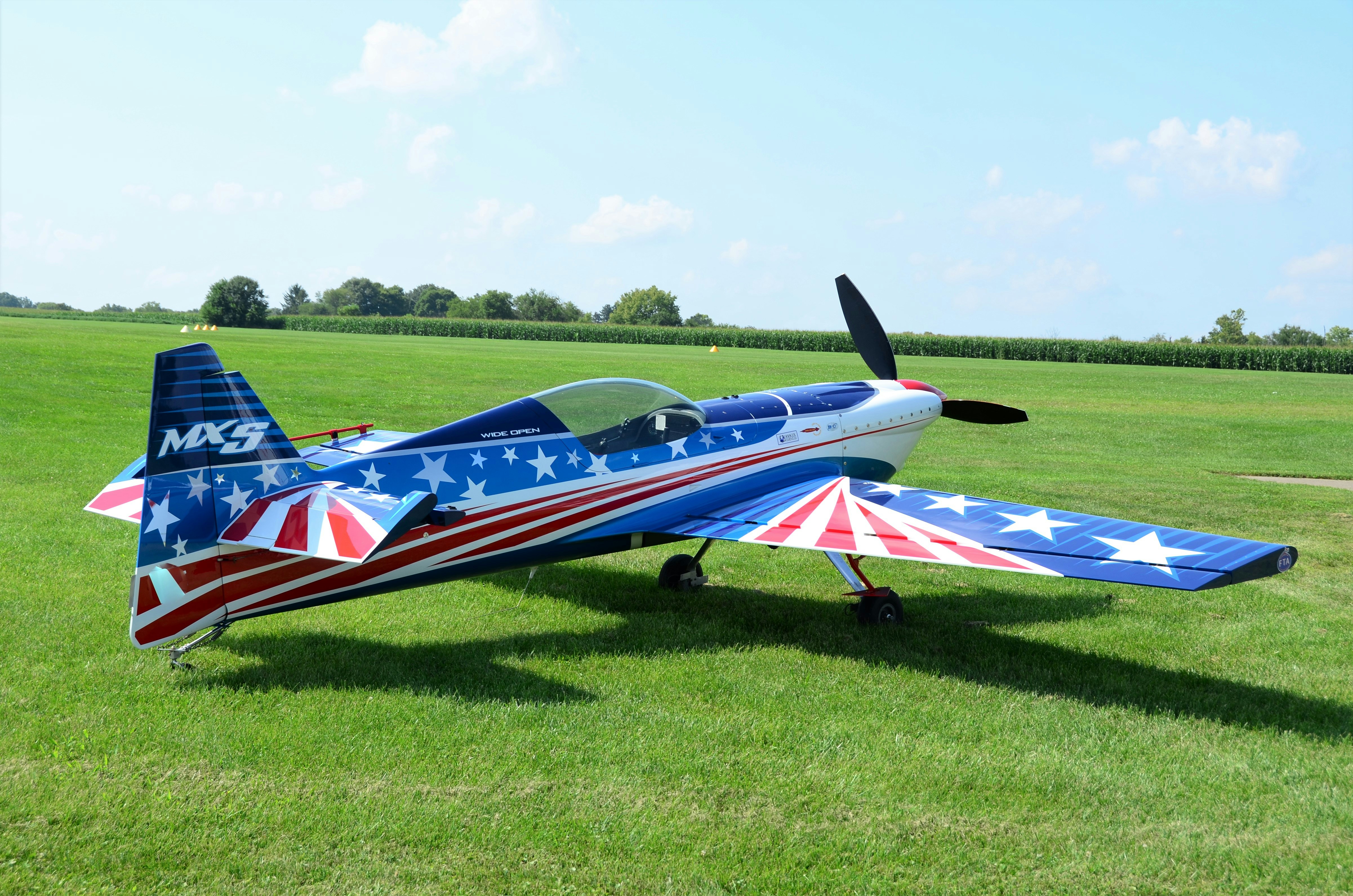 A blue and red plane sitting on top of a lush green field photo – Free ...