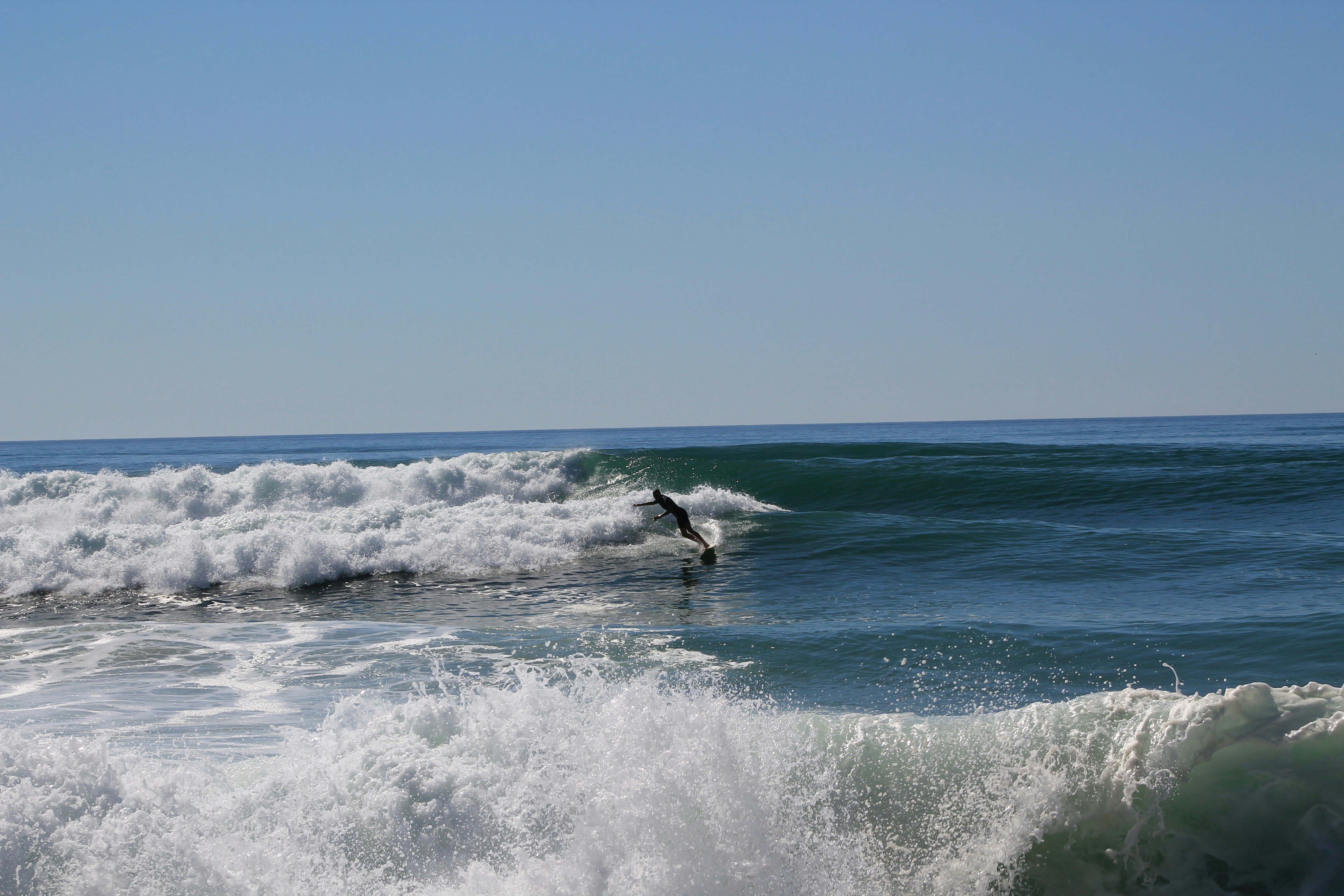 Surfer skillfully maneuvering on a large ocean wave under a clear blue sky.