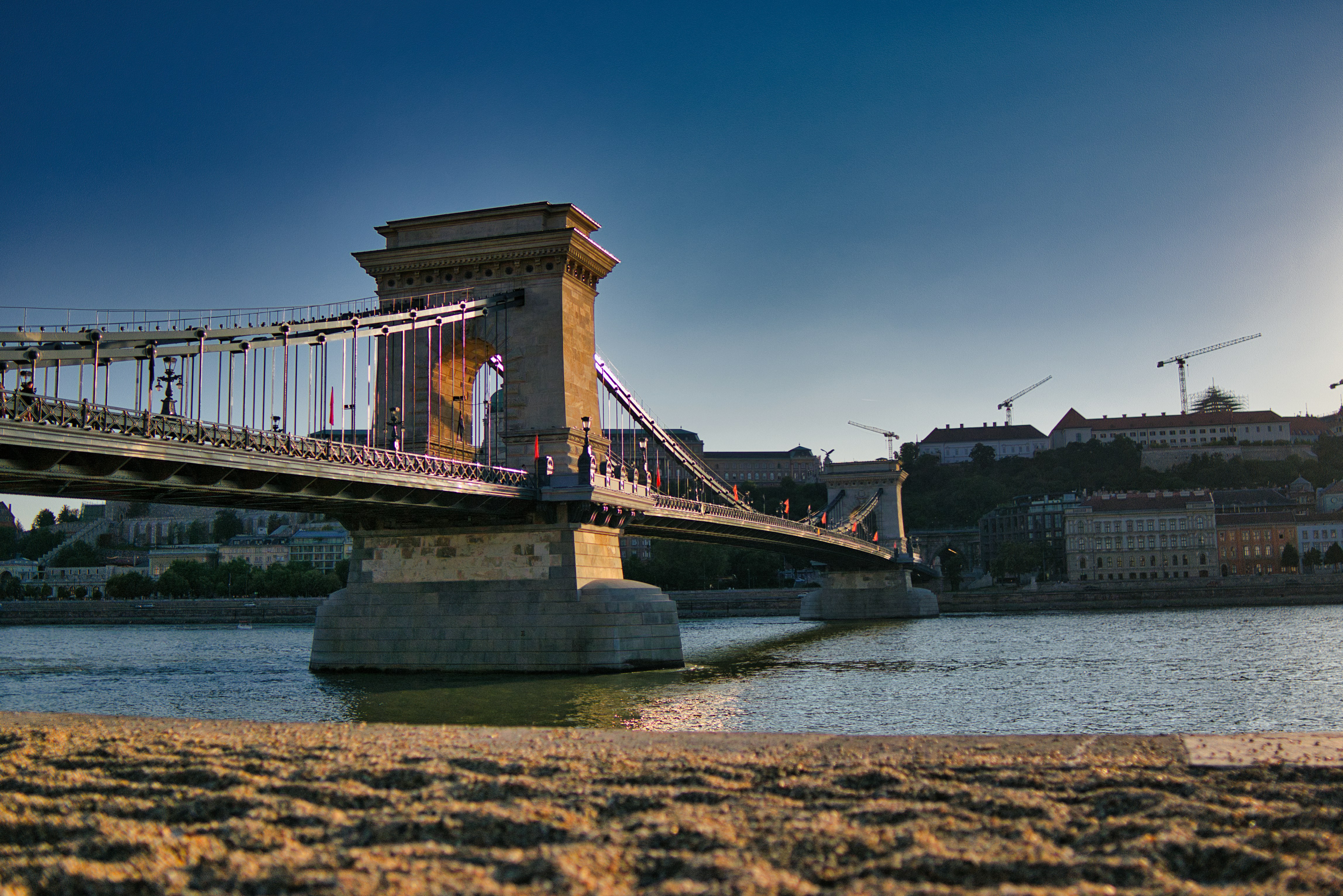 View of Szechenyi Lanchid from Budapest, Hungary. | a bridge over a body of water with buildings in the background