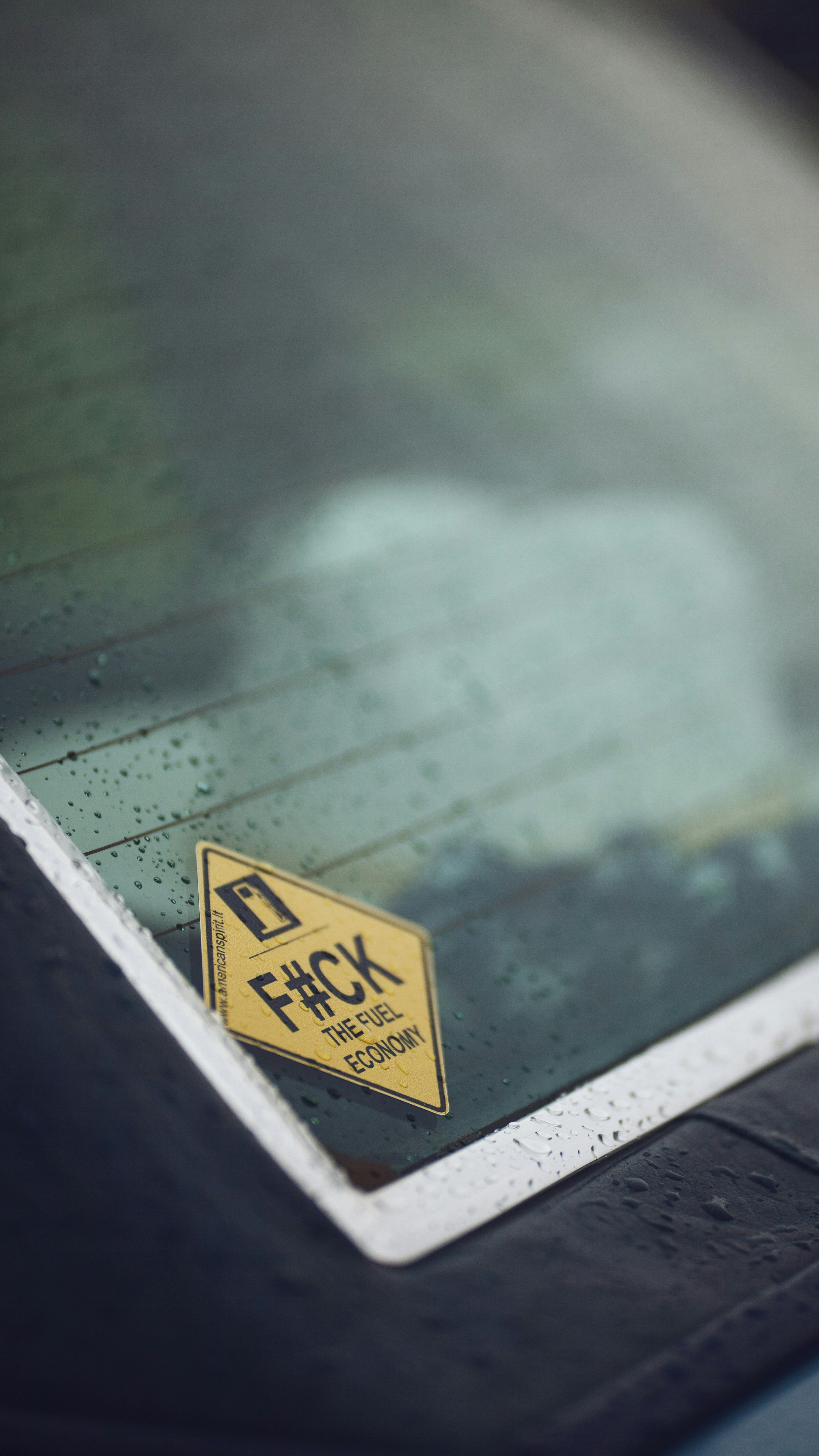 F#CK the Fuel Economy: A Rain-Slick Protest Sticker on a Car Window