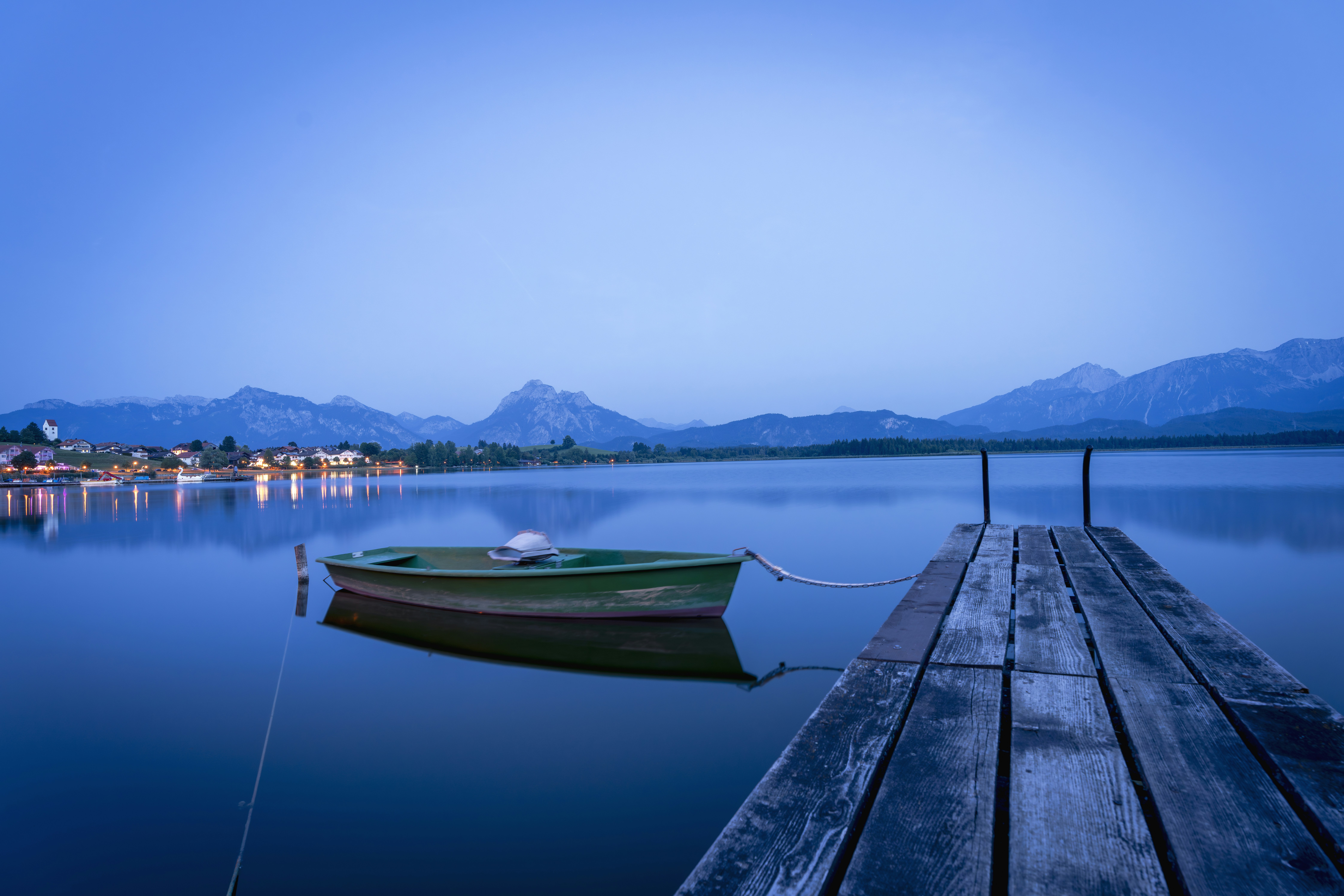A small green boat tethered to a wooden dock on a serene lake under a twilight sky.