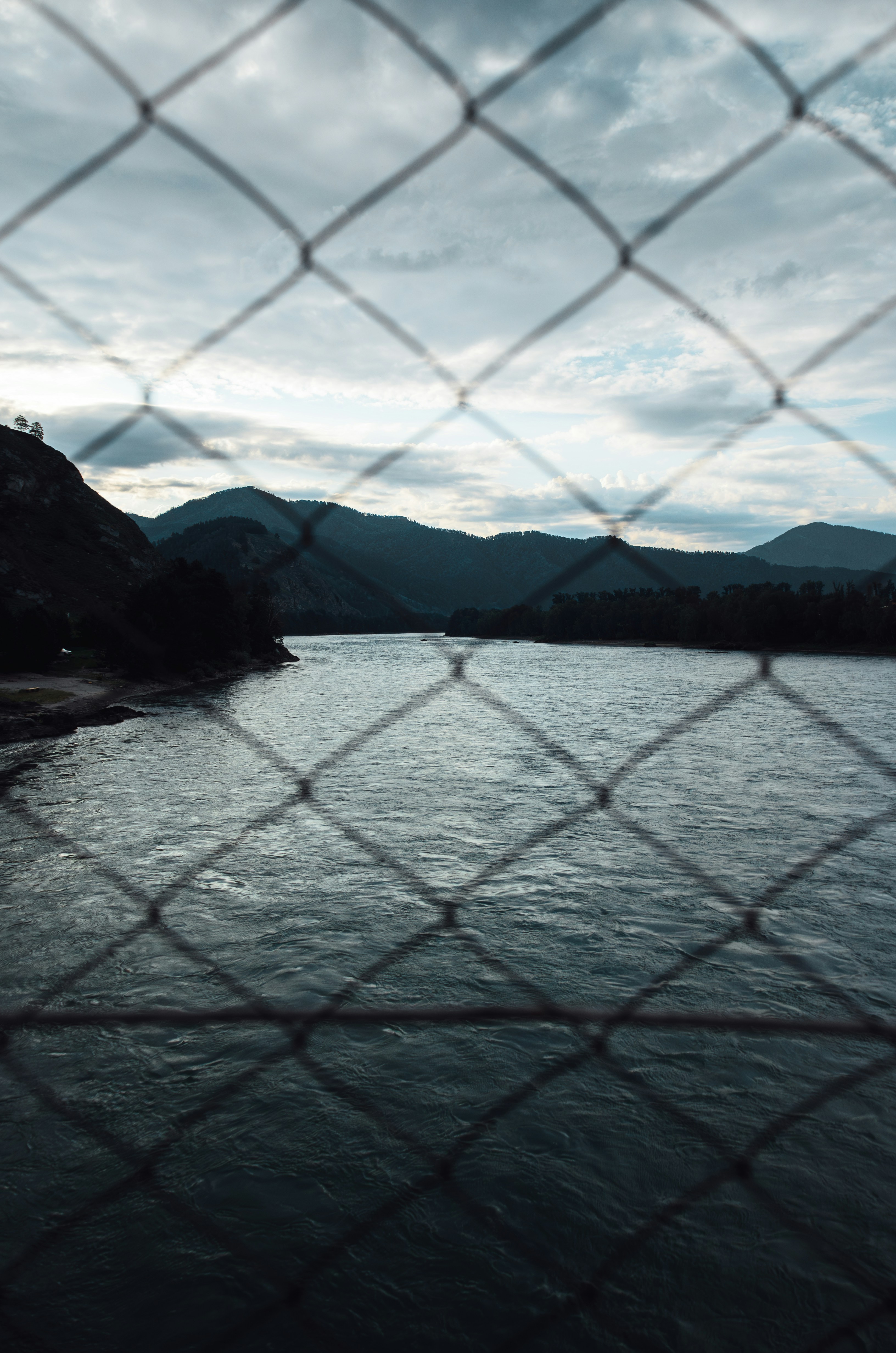 Grid of Water and Distant Hills Framed by a Chain-Link Veil