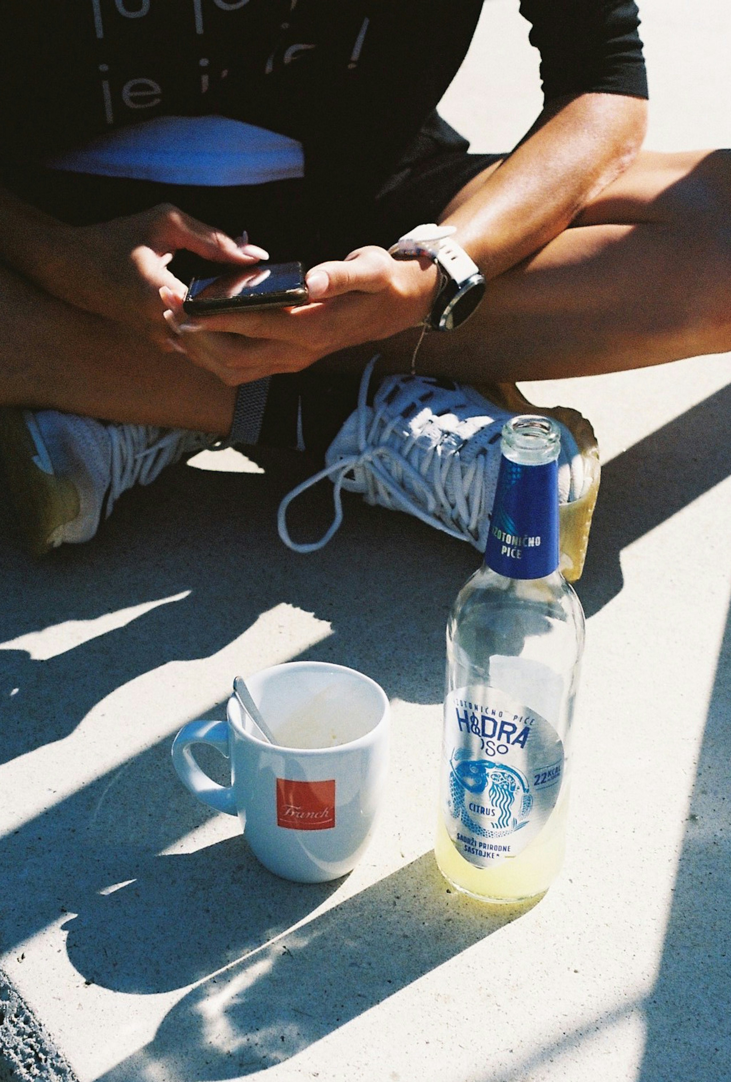 Sunlit Pause: A Phone, a Cup, and a Lemon Soda on Concrete