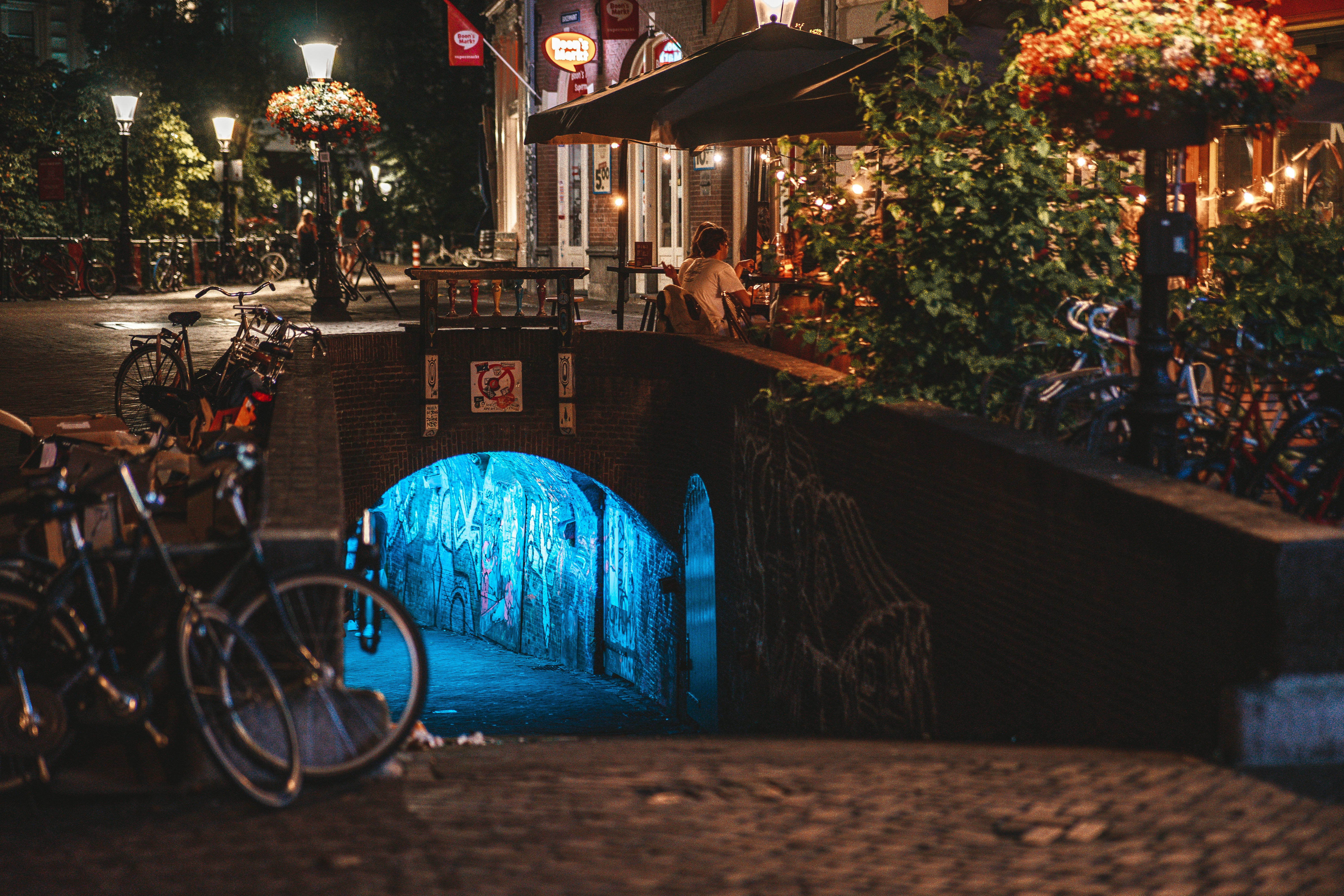 Blue Arch at Night: Cobblestone Bridge Framing a Cozy City Dining Scene