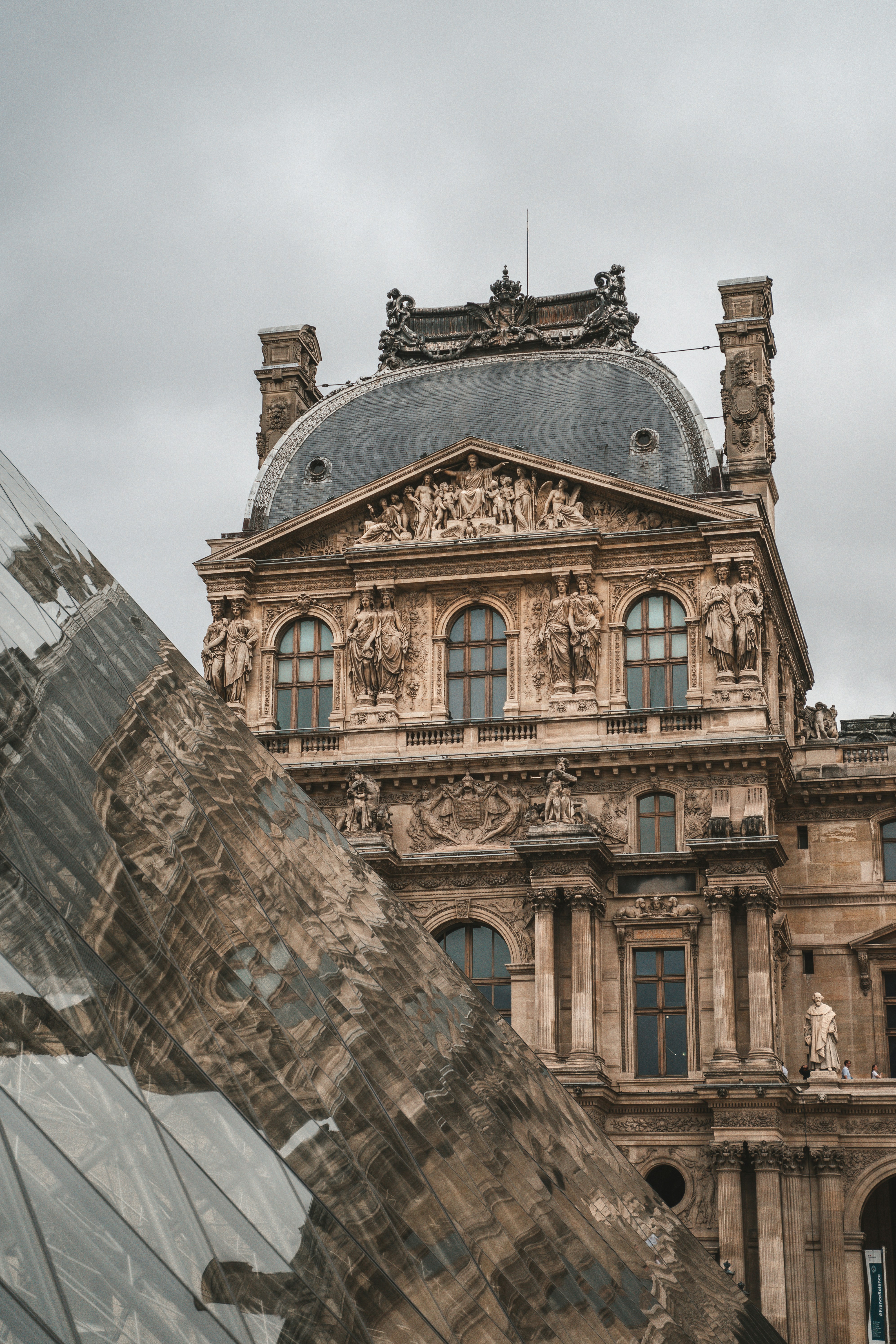 Louvre Facade Framed by the Glass Pyramid Beneath an Overcast Sky