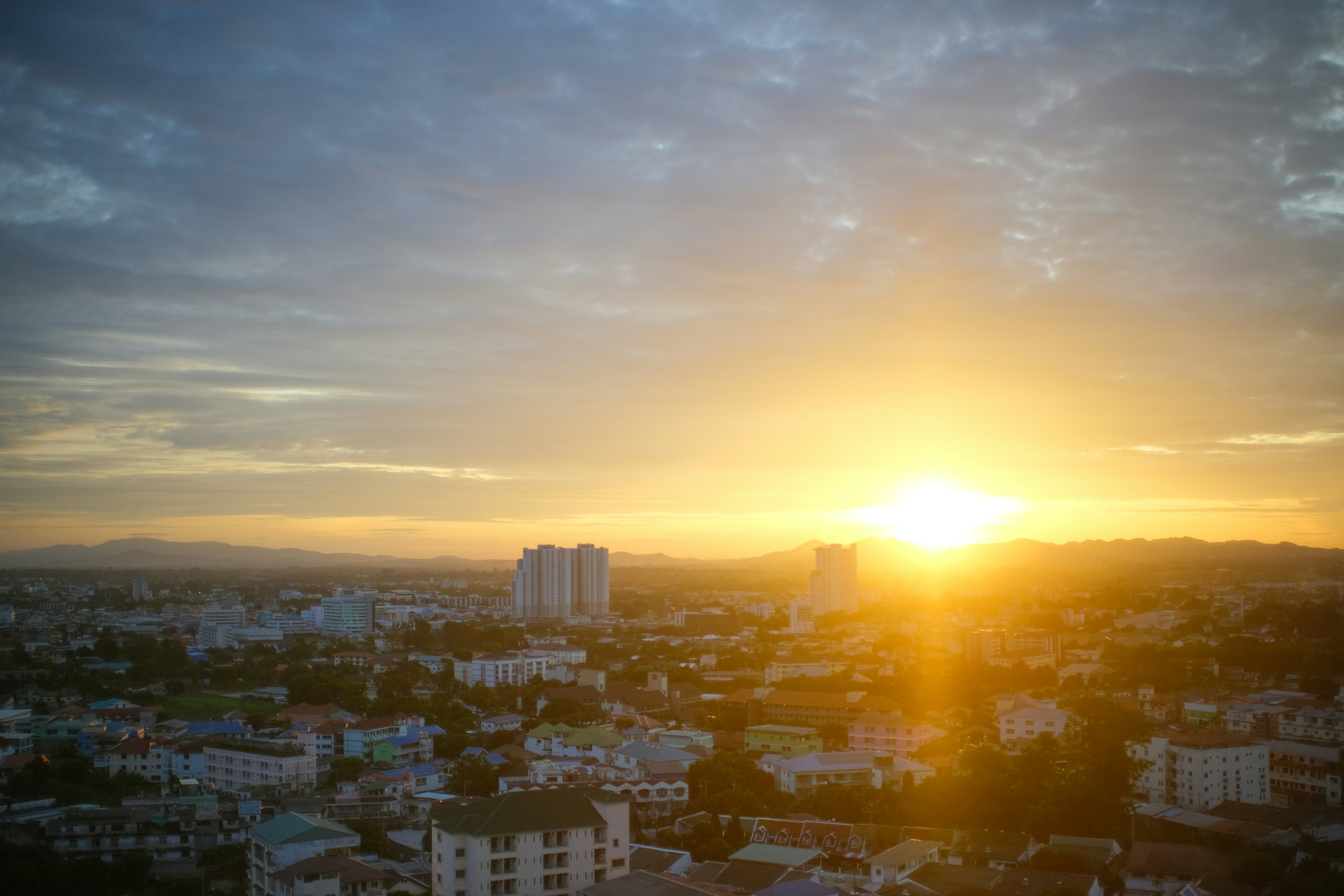 Sunset casting a warm glow over a cityscape with tall buildings and a cloudy sky.