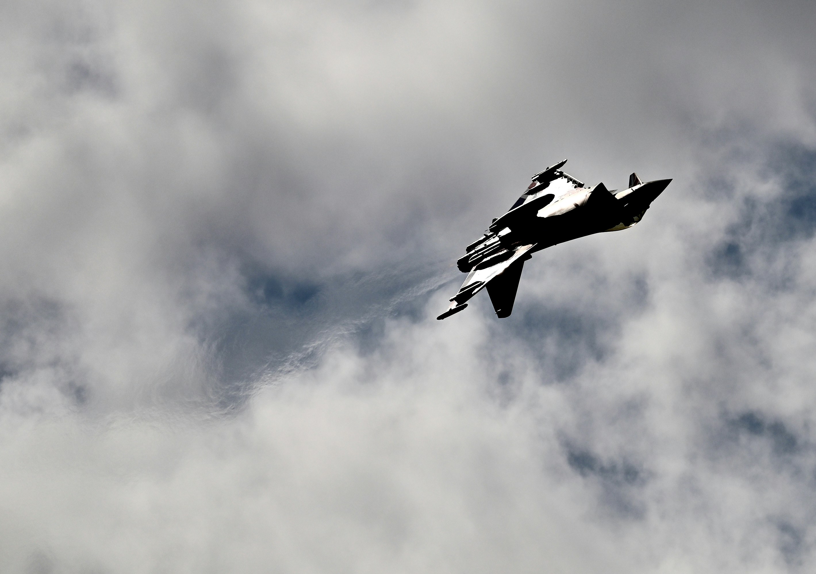 Jet silhouette slicing through sunlit clouds
