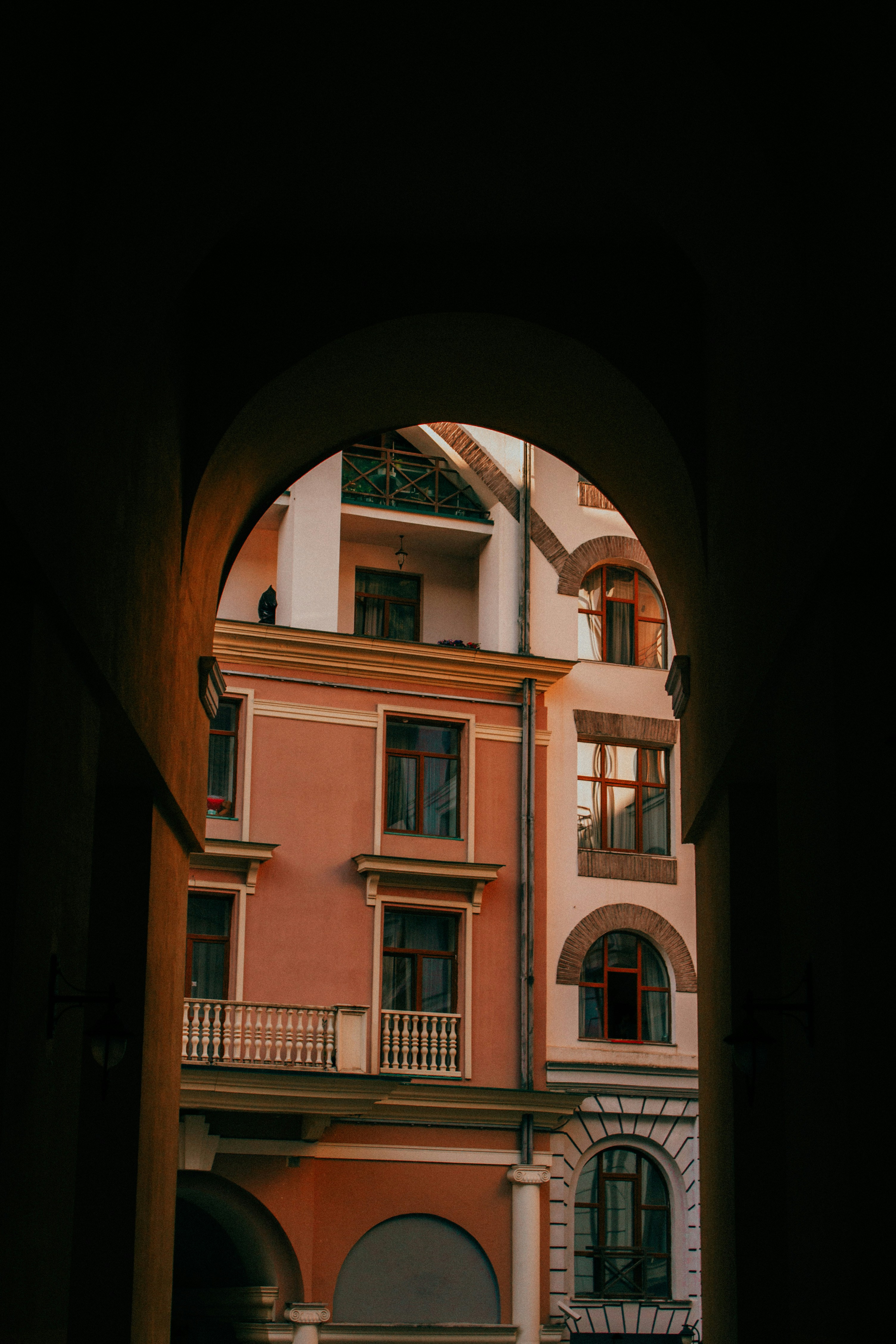 Archway Reverie: Sunlit Peach Facade Framed by a Shadowed Corridor