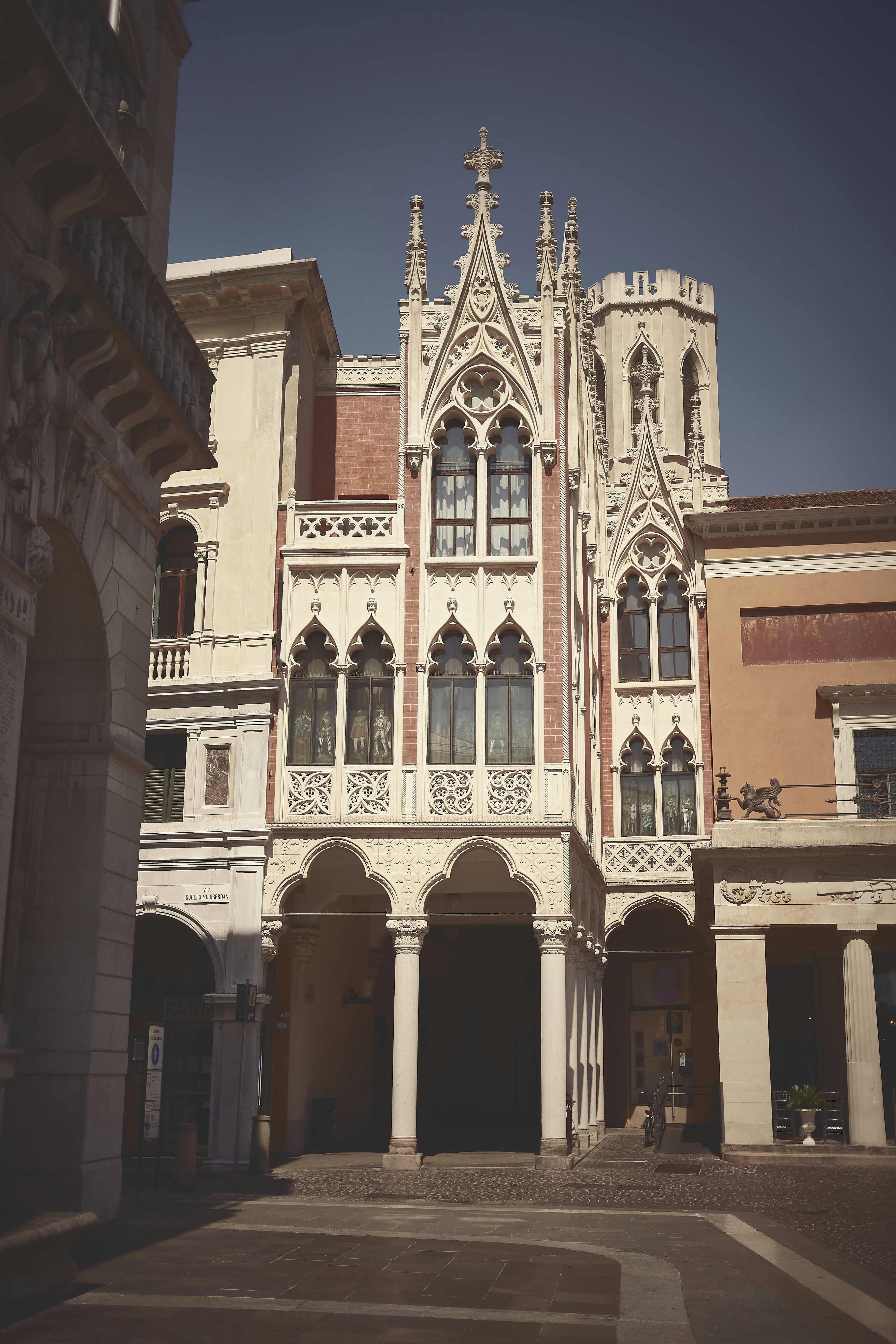 Spire-Crowned Facade: Arched Arcade and Lacework Stonework in a Sunlit Gothic Courtyard