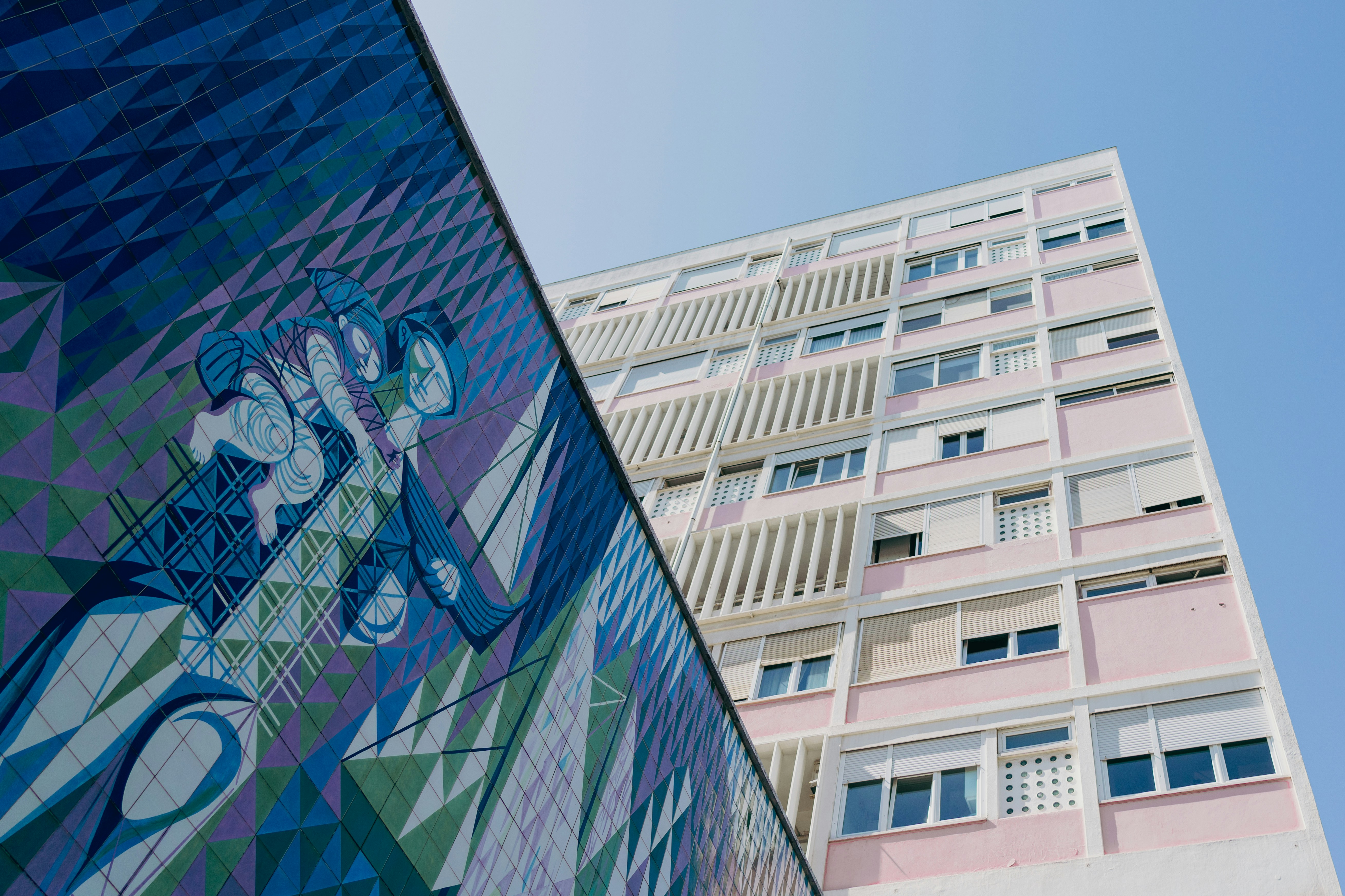 Vibrant mural juxtaposed with a pastel high-rise building against a clear blue sky.