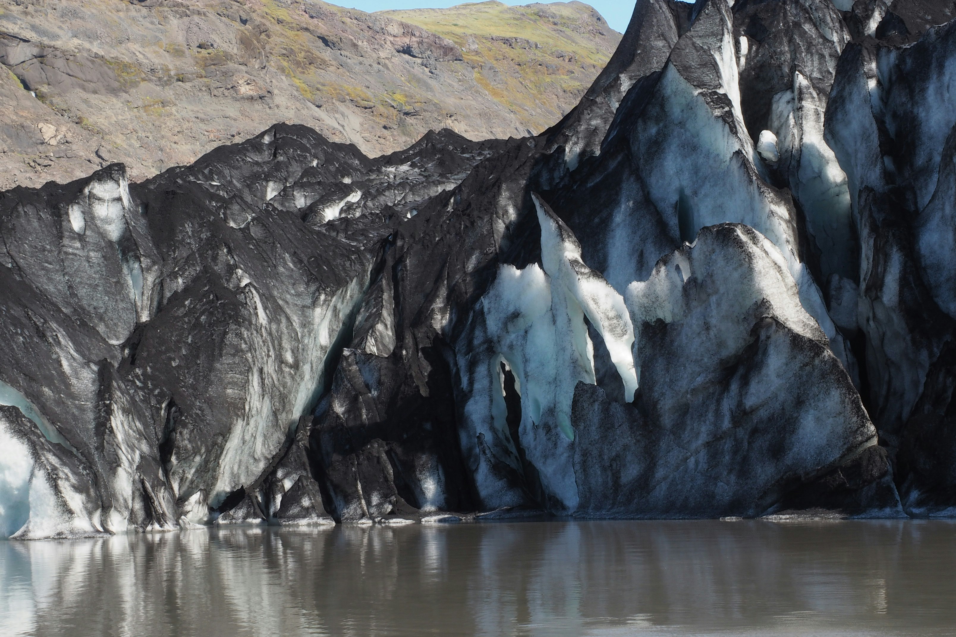 Glacier with blue-ice towers reflected on calm water, highlighting stark contrast and natural sculpting.