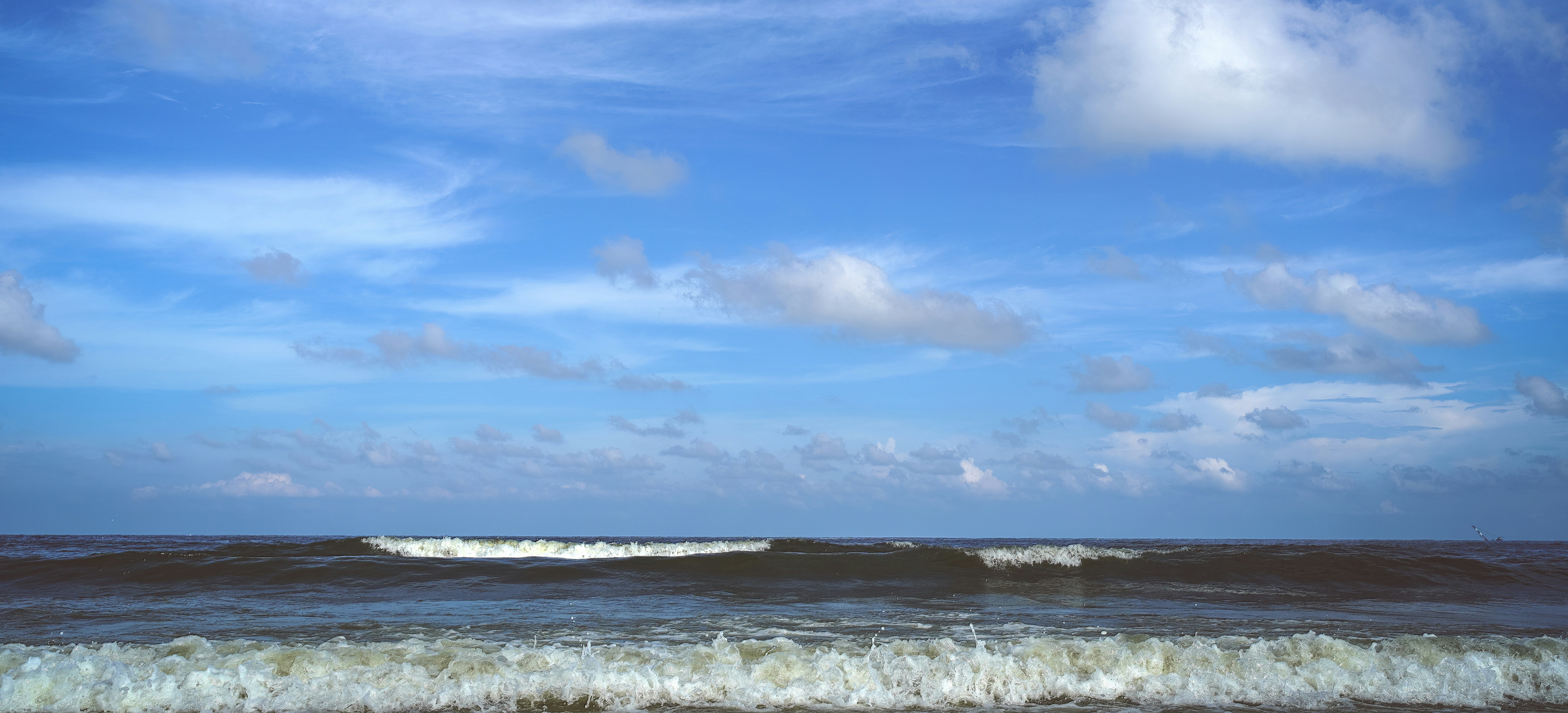 Calm ocean waves under a bright blue sky with scattered clouds.