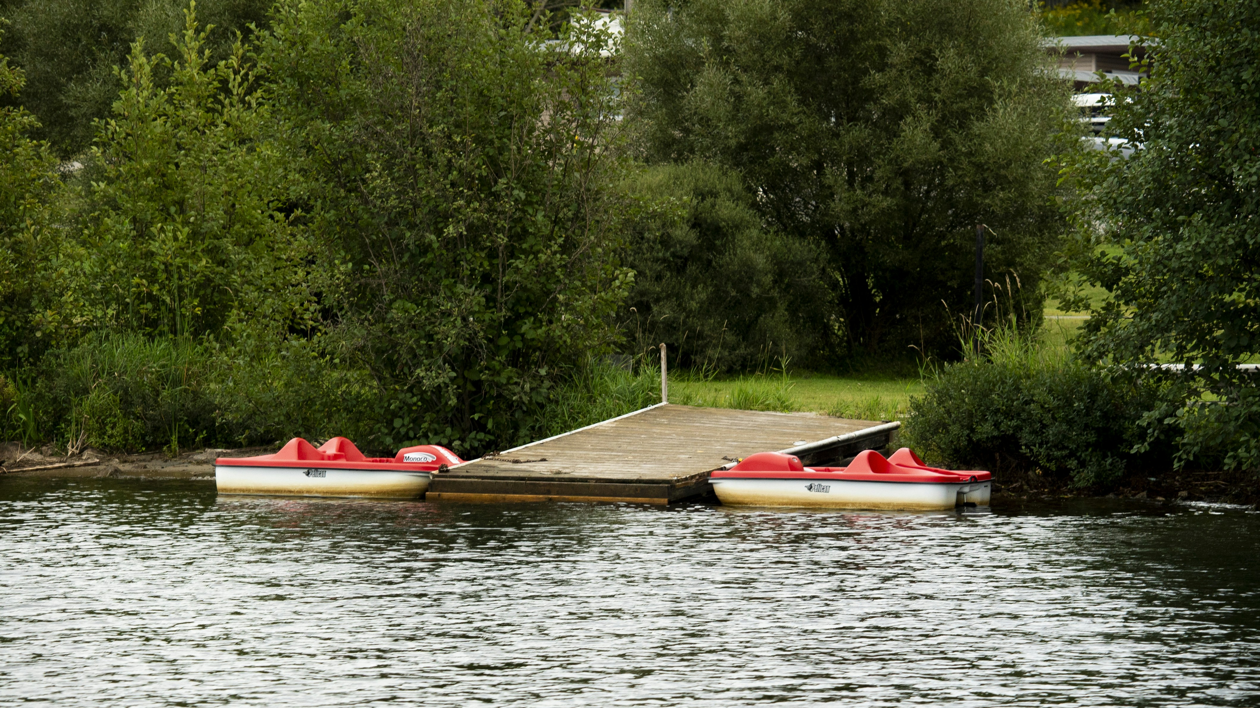 Twin Crimson Pedal Boats Rest at a Quiet Riverside Dock