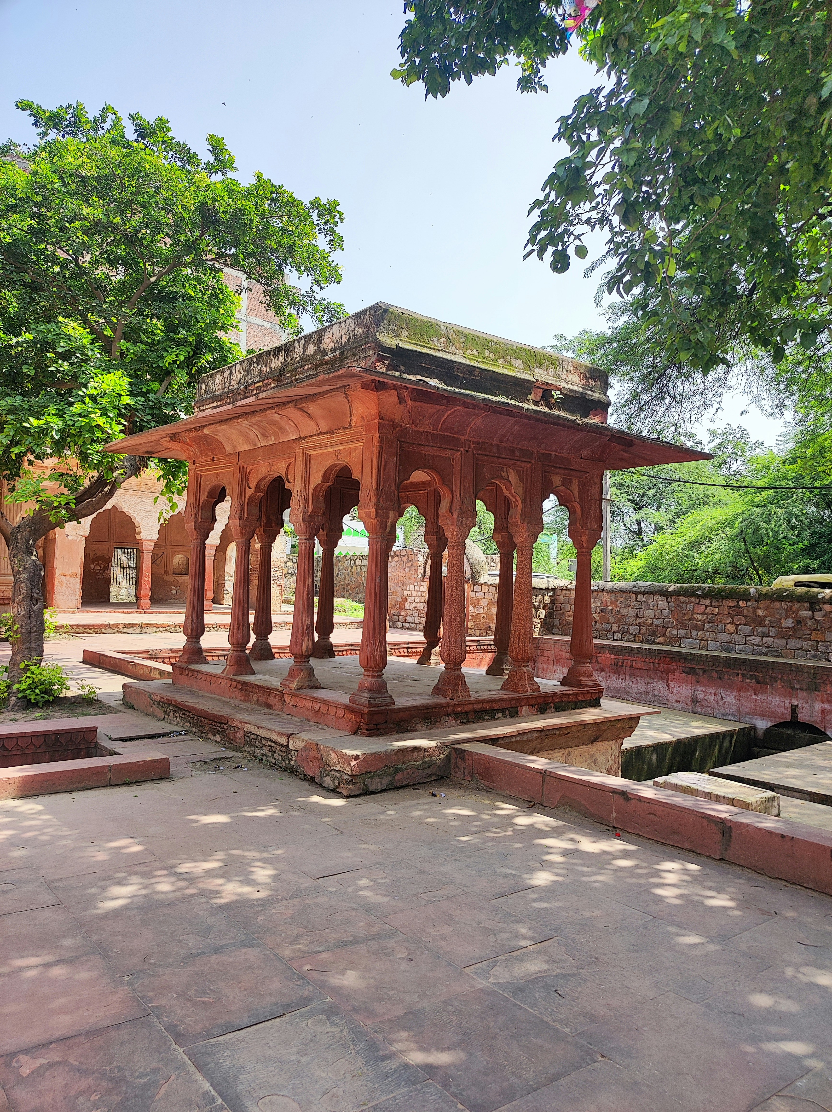 Intricate red sandstone pavilion surrounded by greenery, showcasing traditional architecture in a tranquil setting.