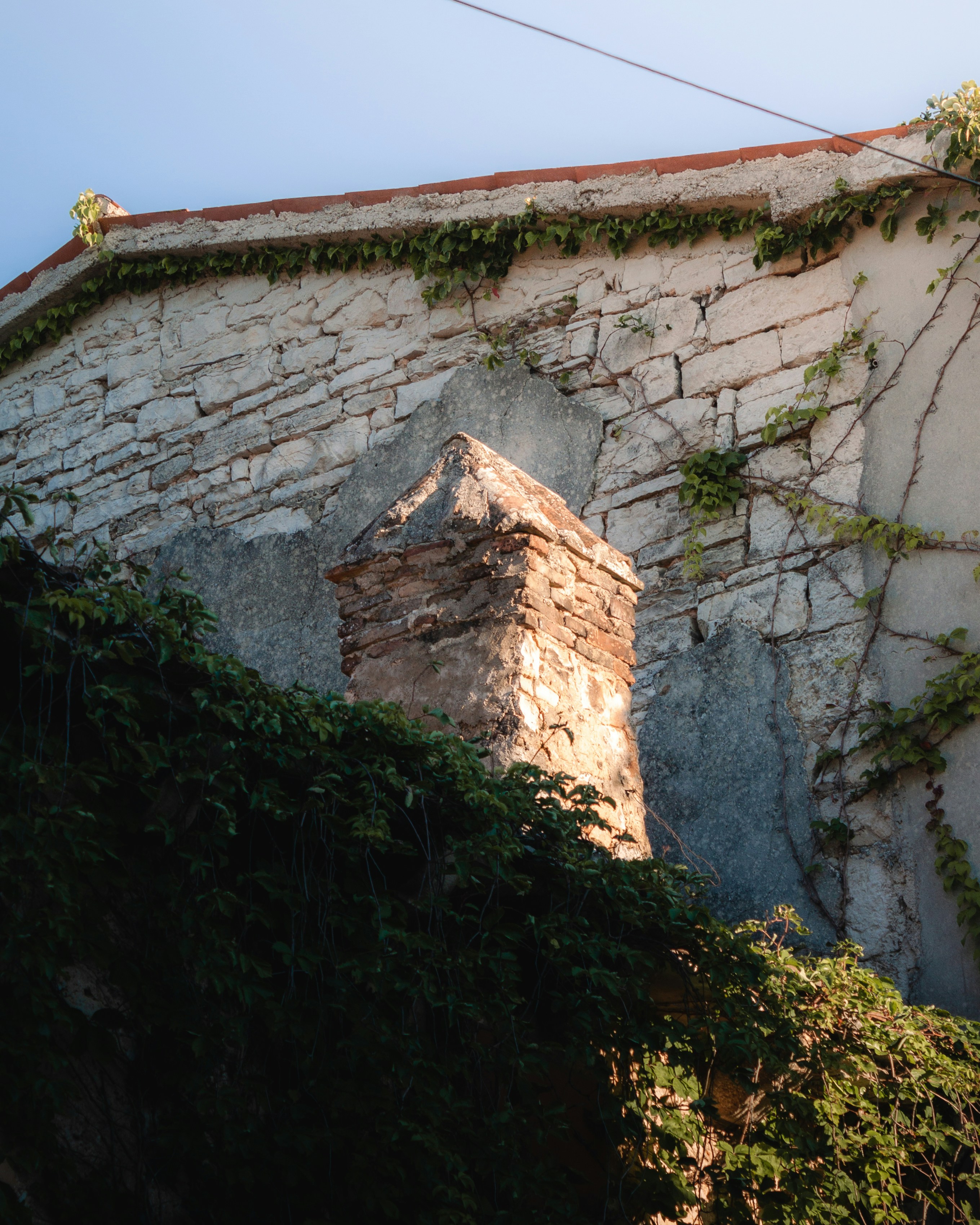 Sunlit Pyramid Pillar Against an Ivy-Covered Stone Wall