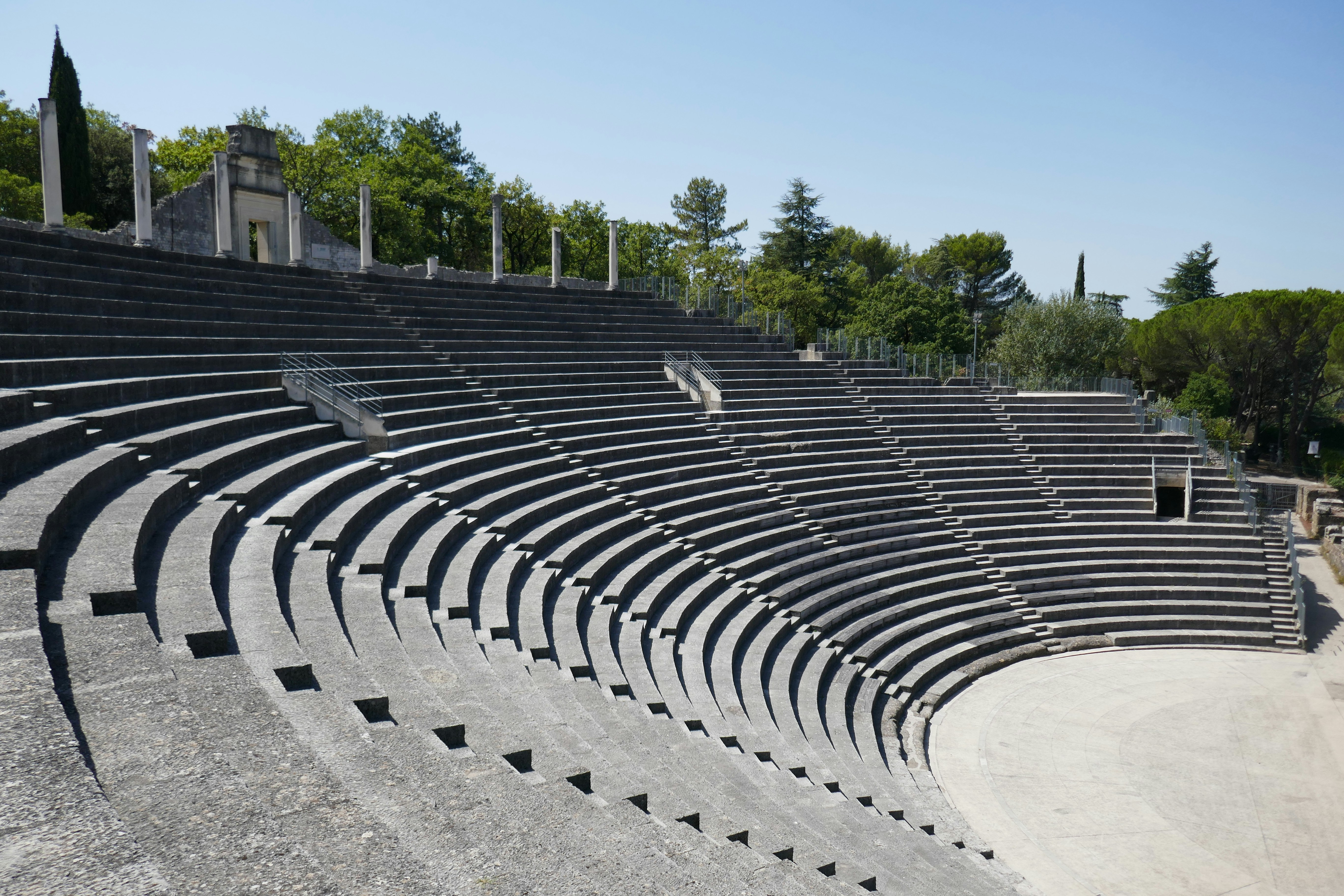 Sunlit stone seats sweep in a semicircle around a bare arena, revealing an ancient amphitheater's curved architecture.